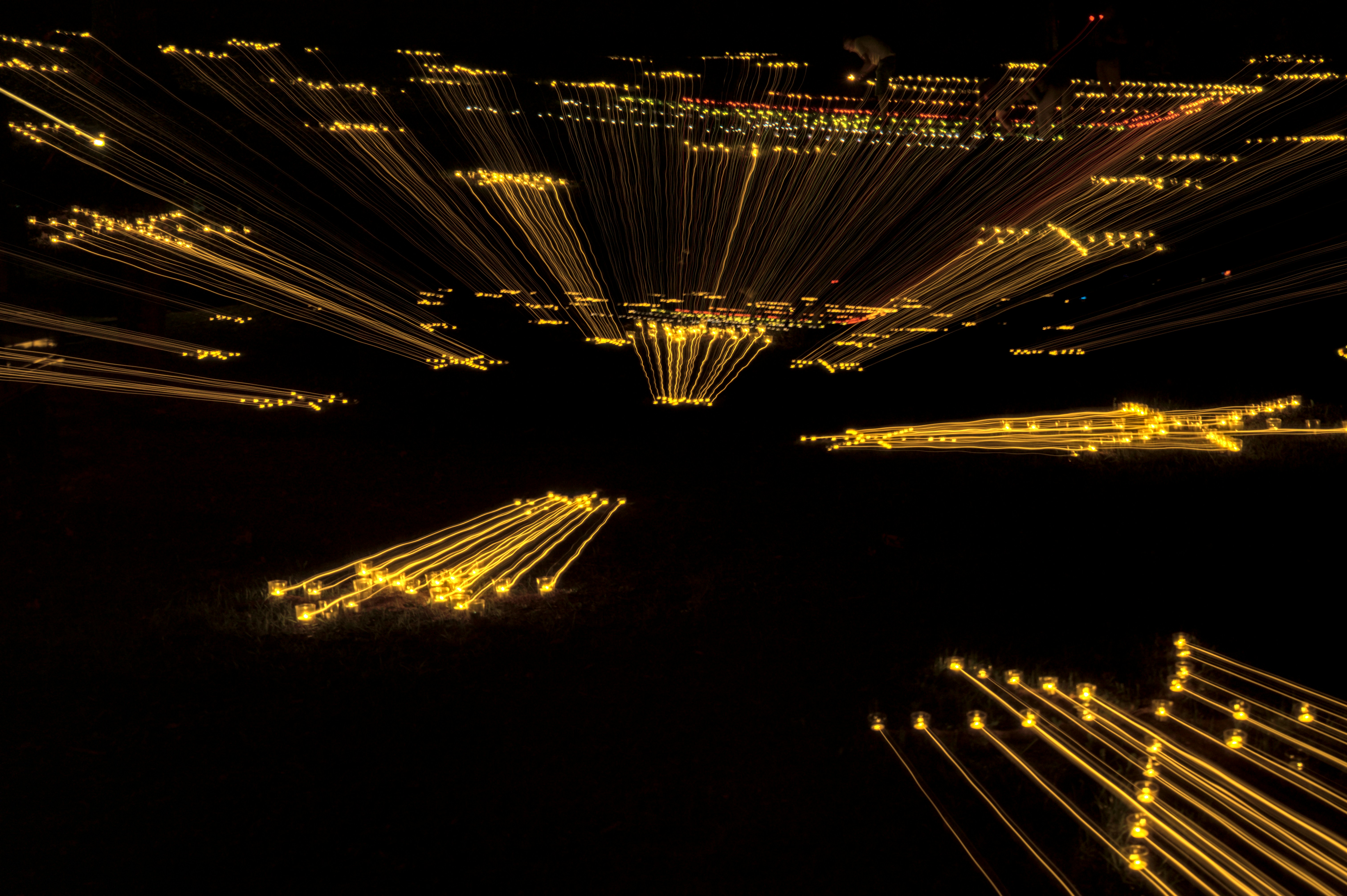 Long-exposure streaks of golden city lights sweep across a dark night, creating radiant lines that converge toward a distant glow.