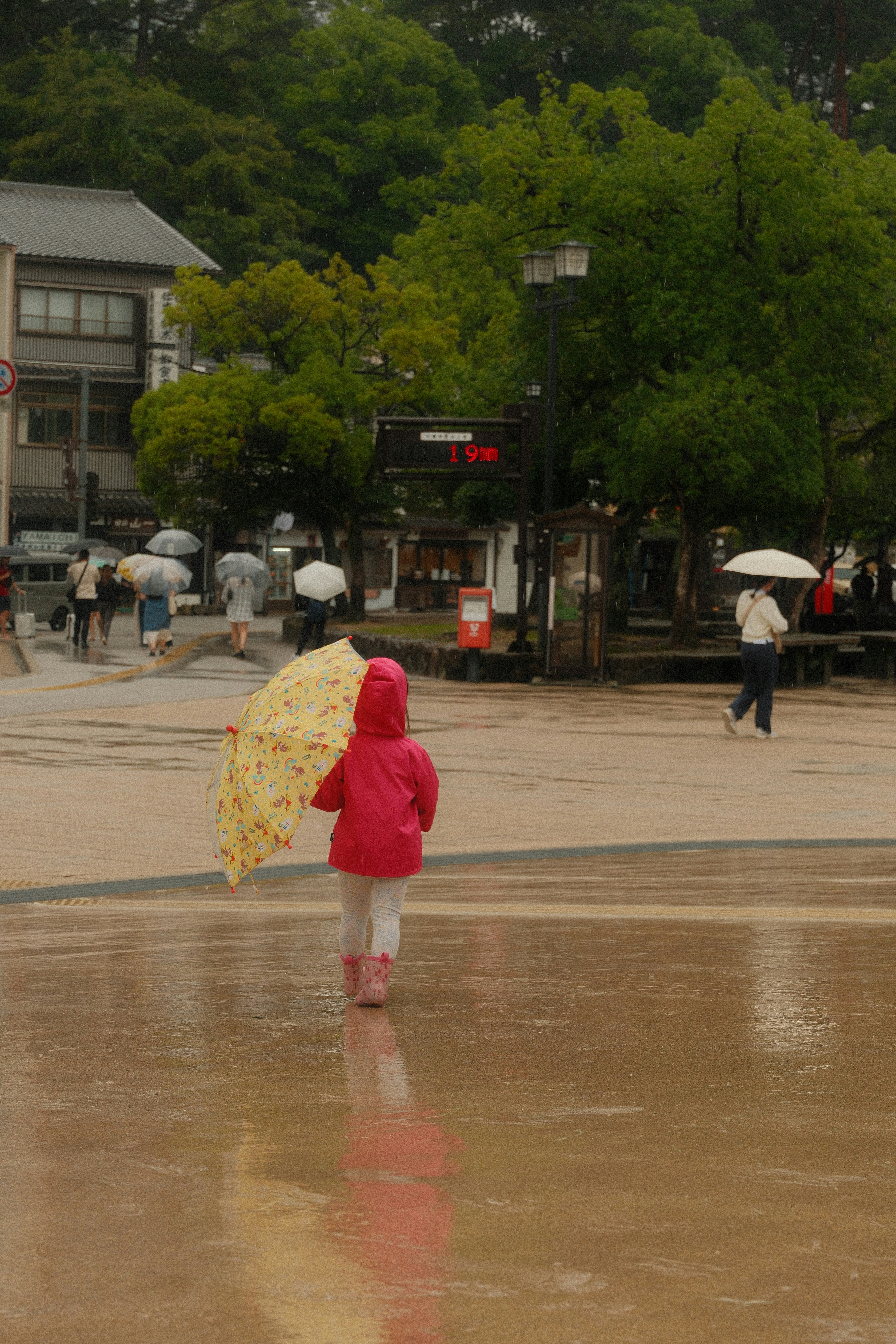 Pink coat, yellow parasol, and rain-soaked plaza: a solitary child in a rainy street scene