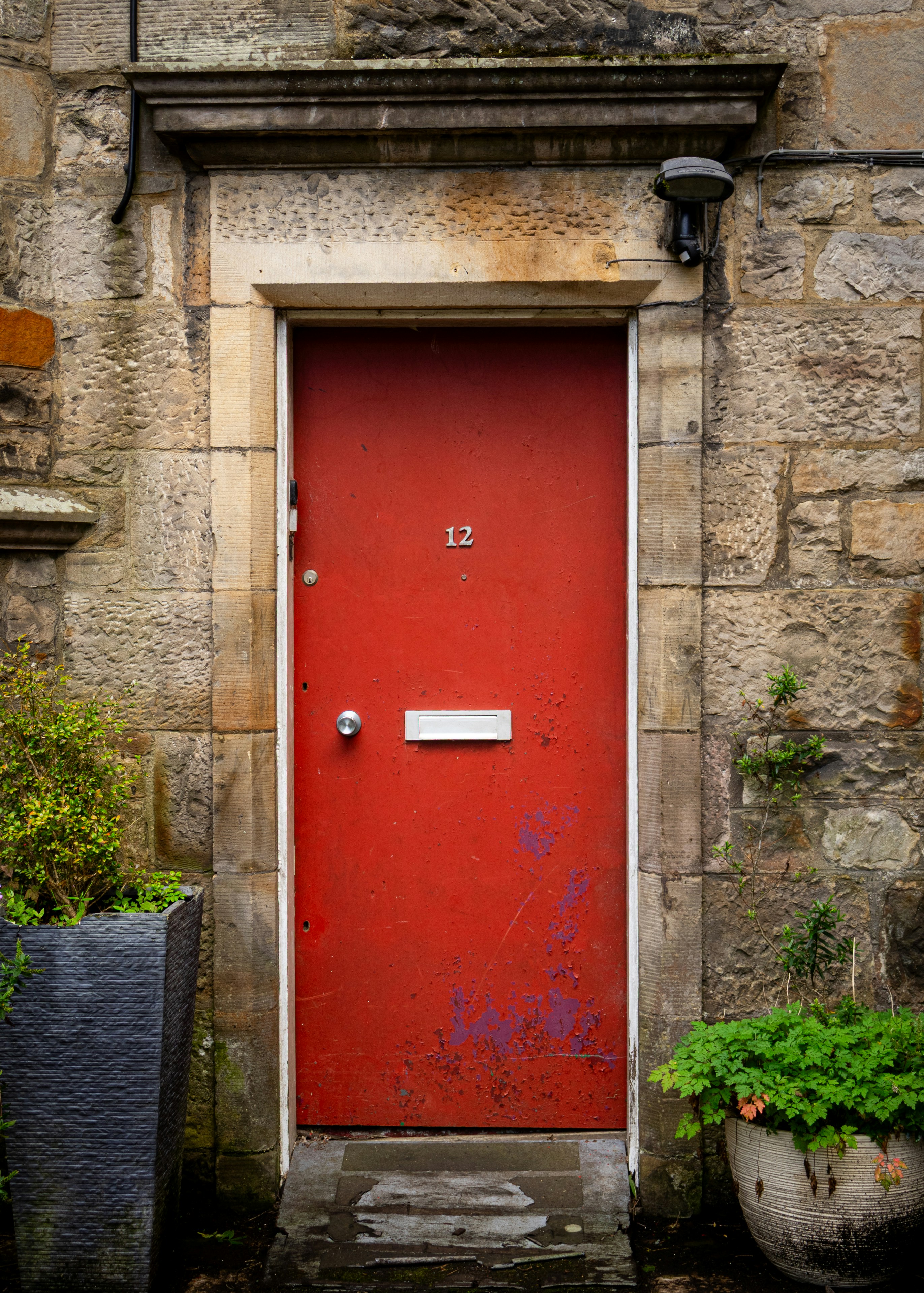 A weathered red door with the number 12 in a stone wall