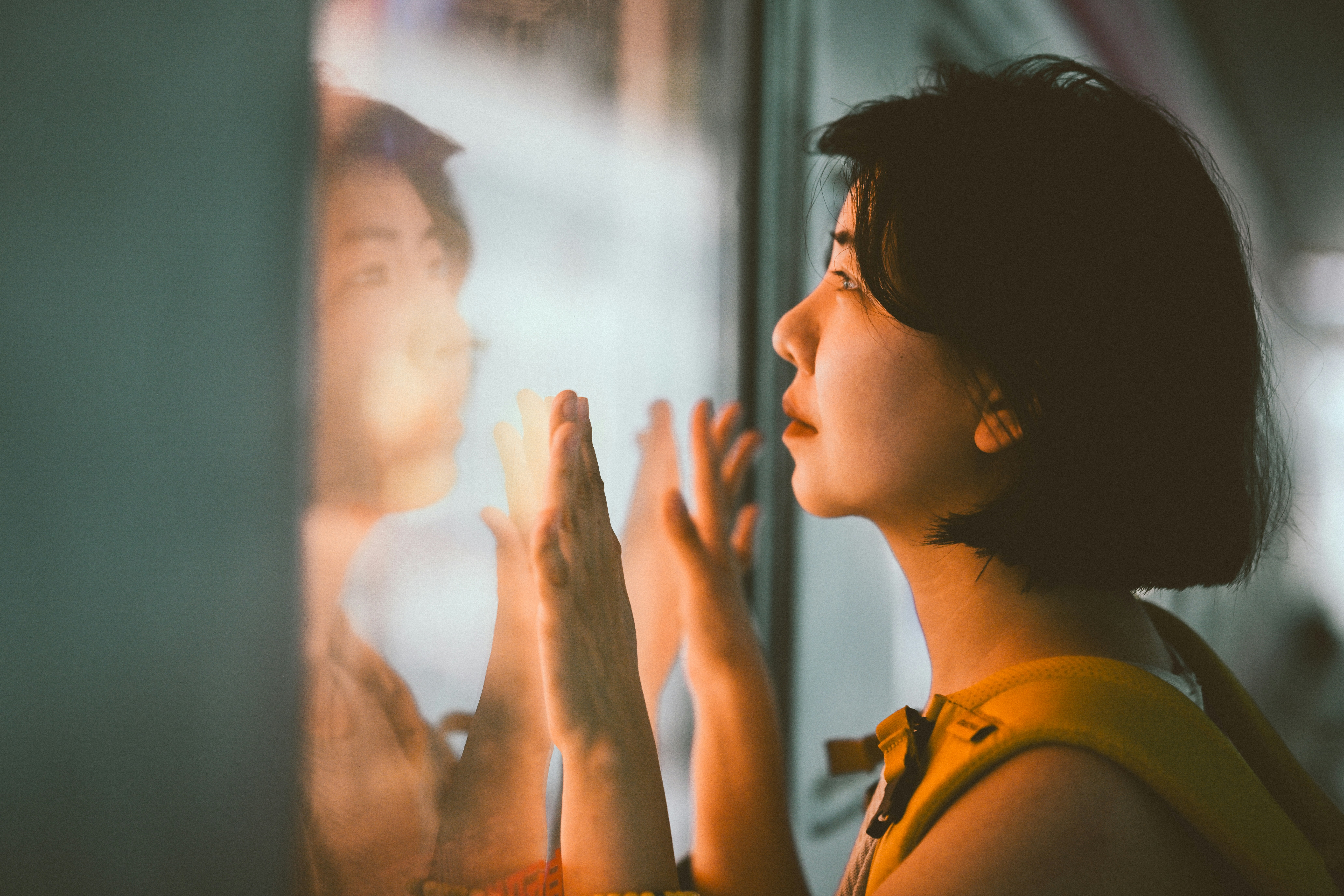 A woman with short dark hair pressing her hands against a glass window