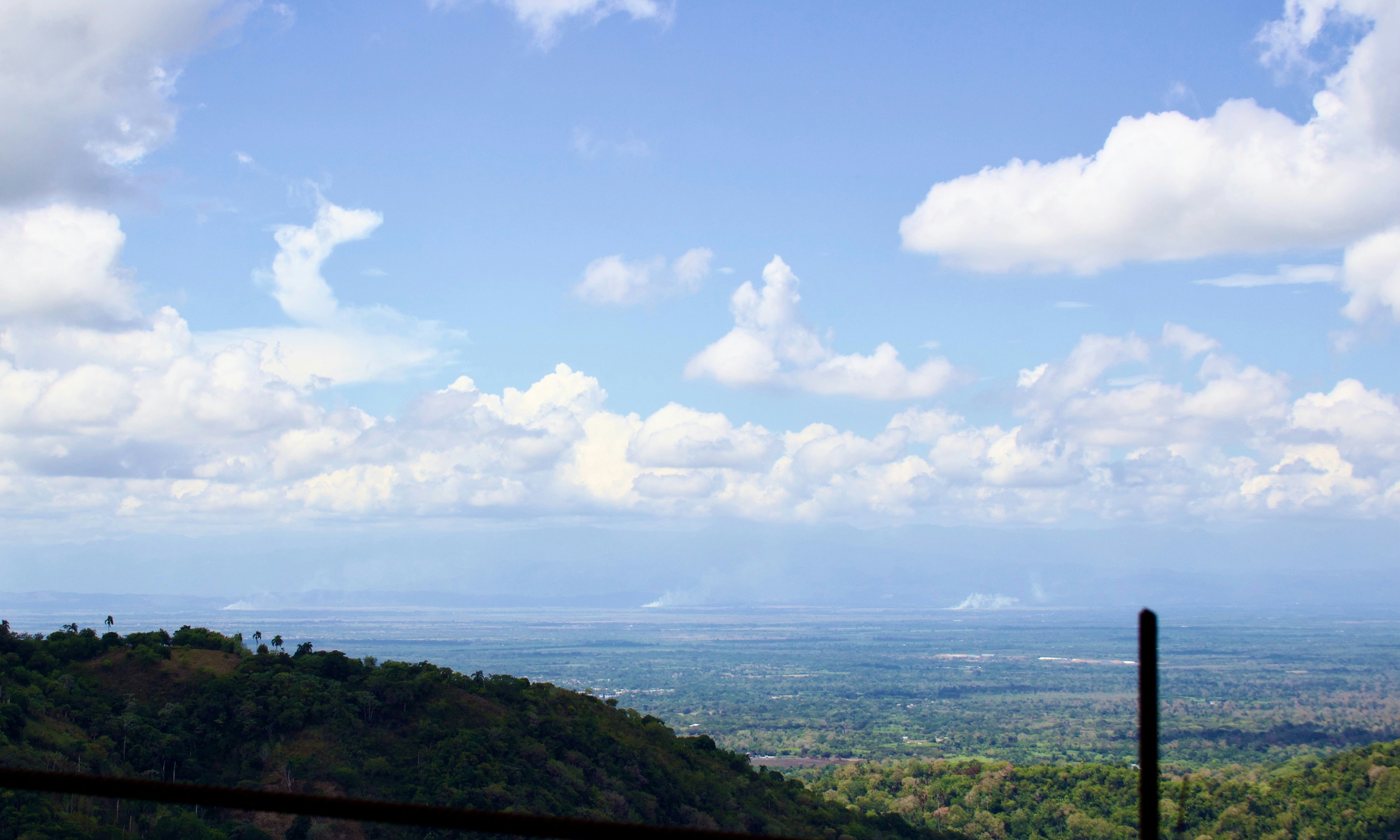 A vast green valley under a bright blue sky with scattered white clouds