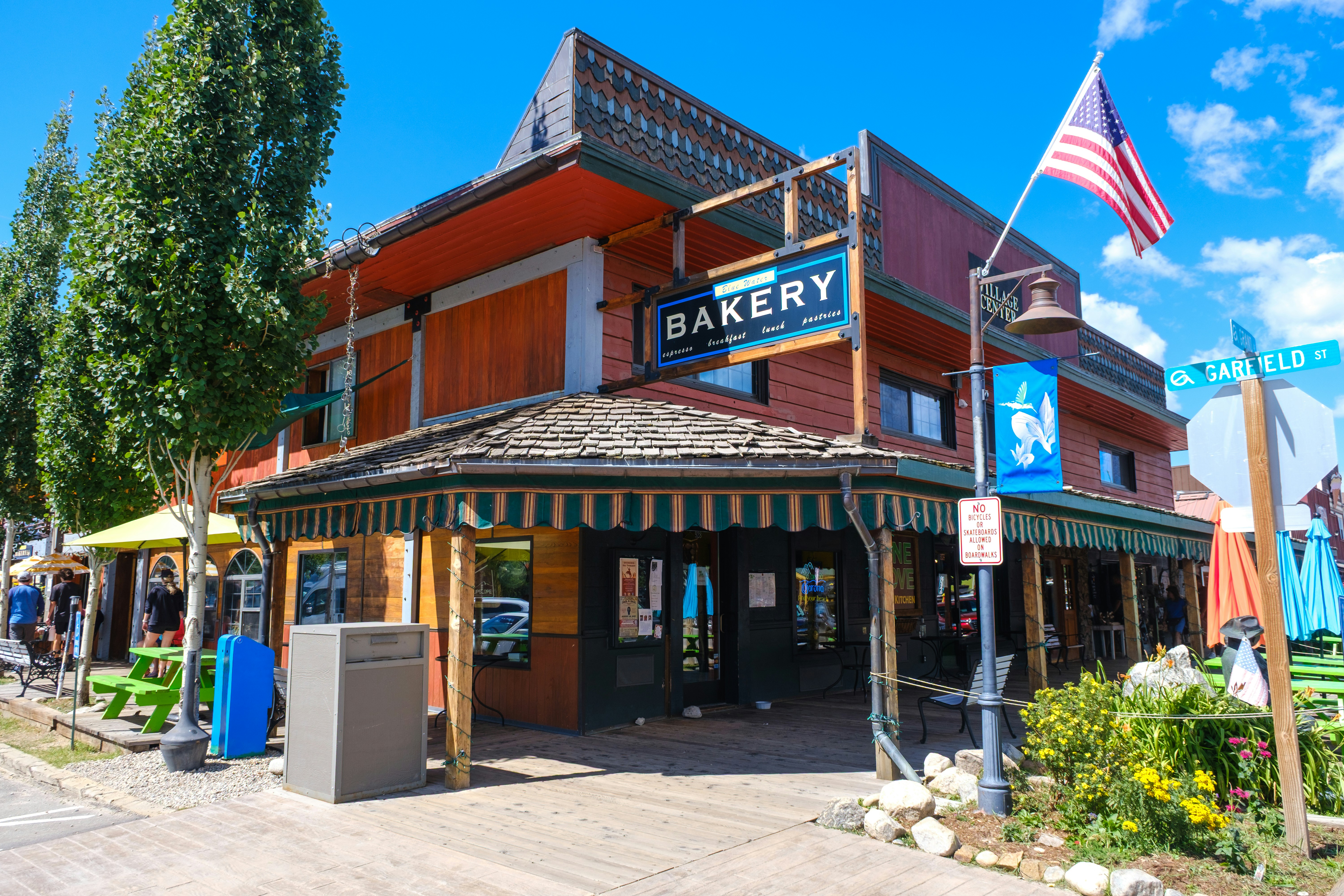 Sunlit Bakery Corner: A Quaint Riverside Stop with Striped Canopy