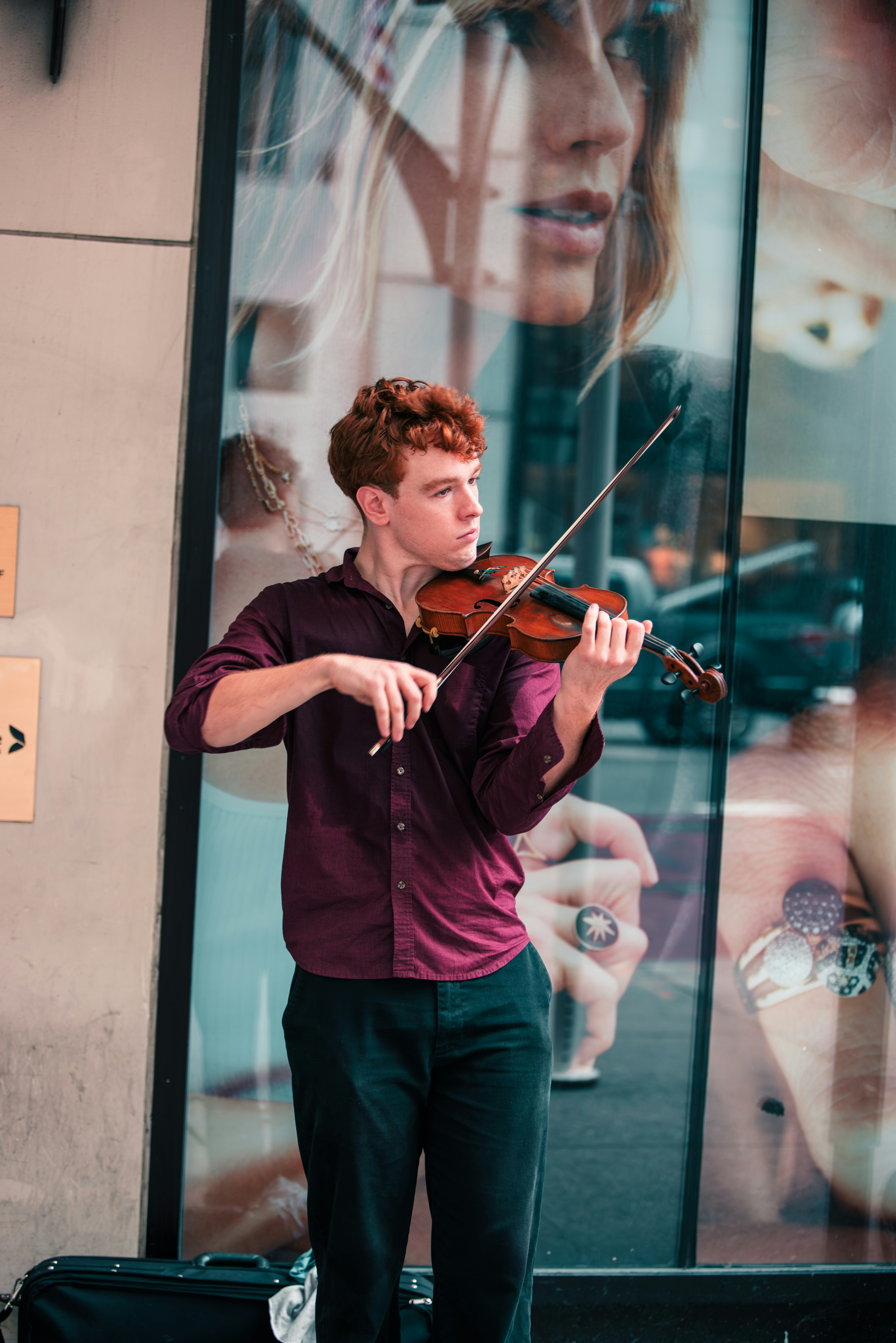 A man with red hair playing a violin in front of a glass storefront