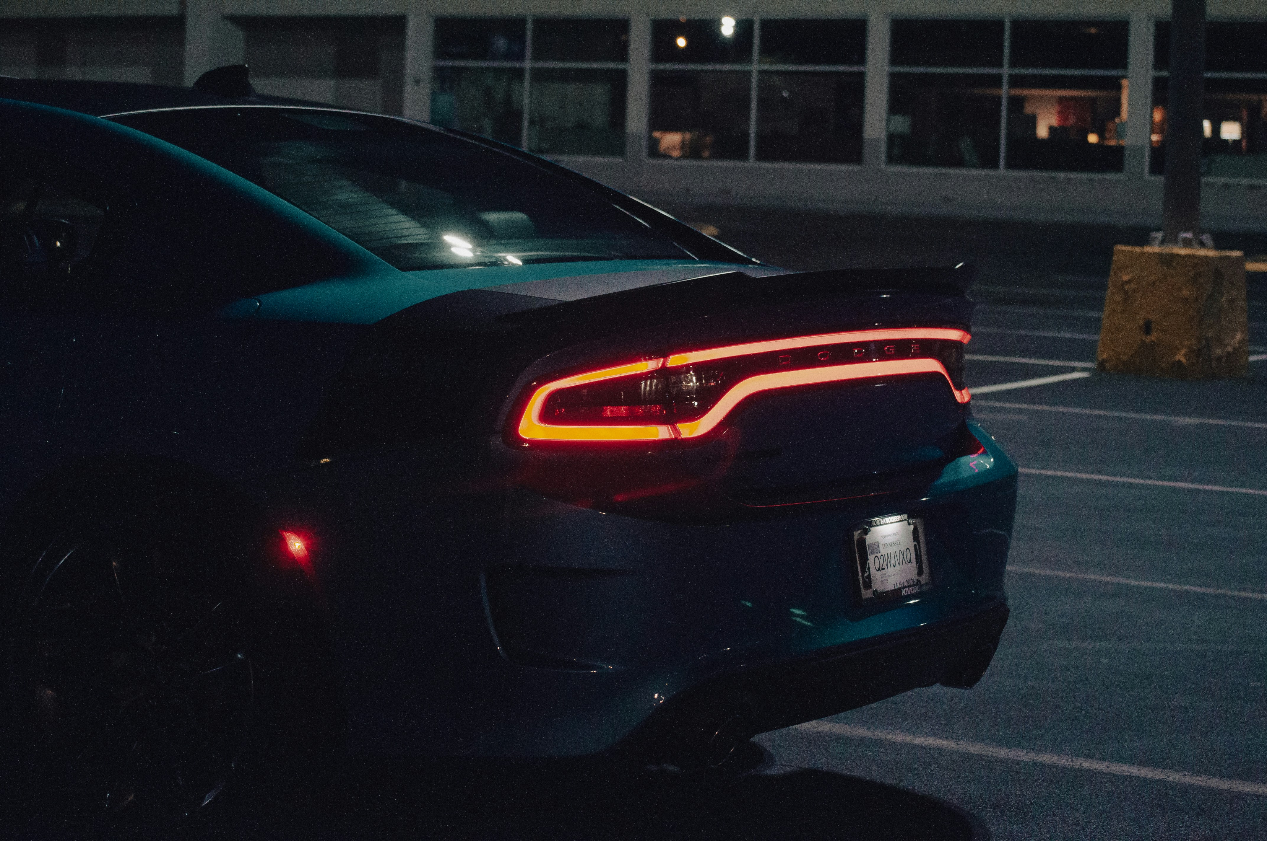 Dark blue car rear with illuminated red taillights in a dim parking lot, highlighting the glowing LED light bar and the vehicle silhouette.