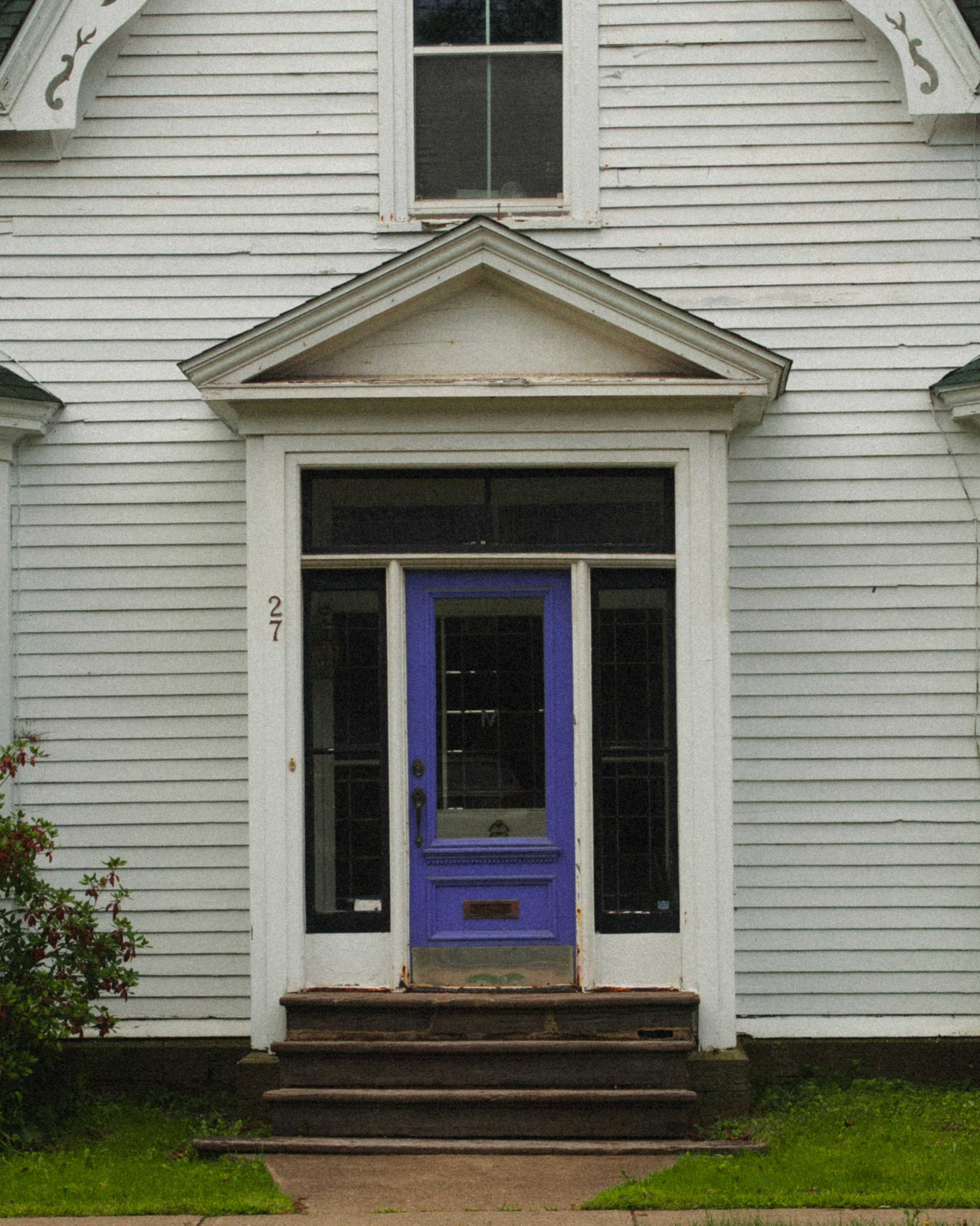Blue door centered within a white clapboard facade, flanked by glass sidelights and a small stoop with steps leading to the entrance.