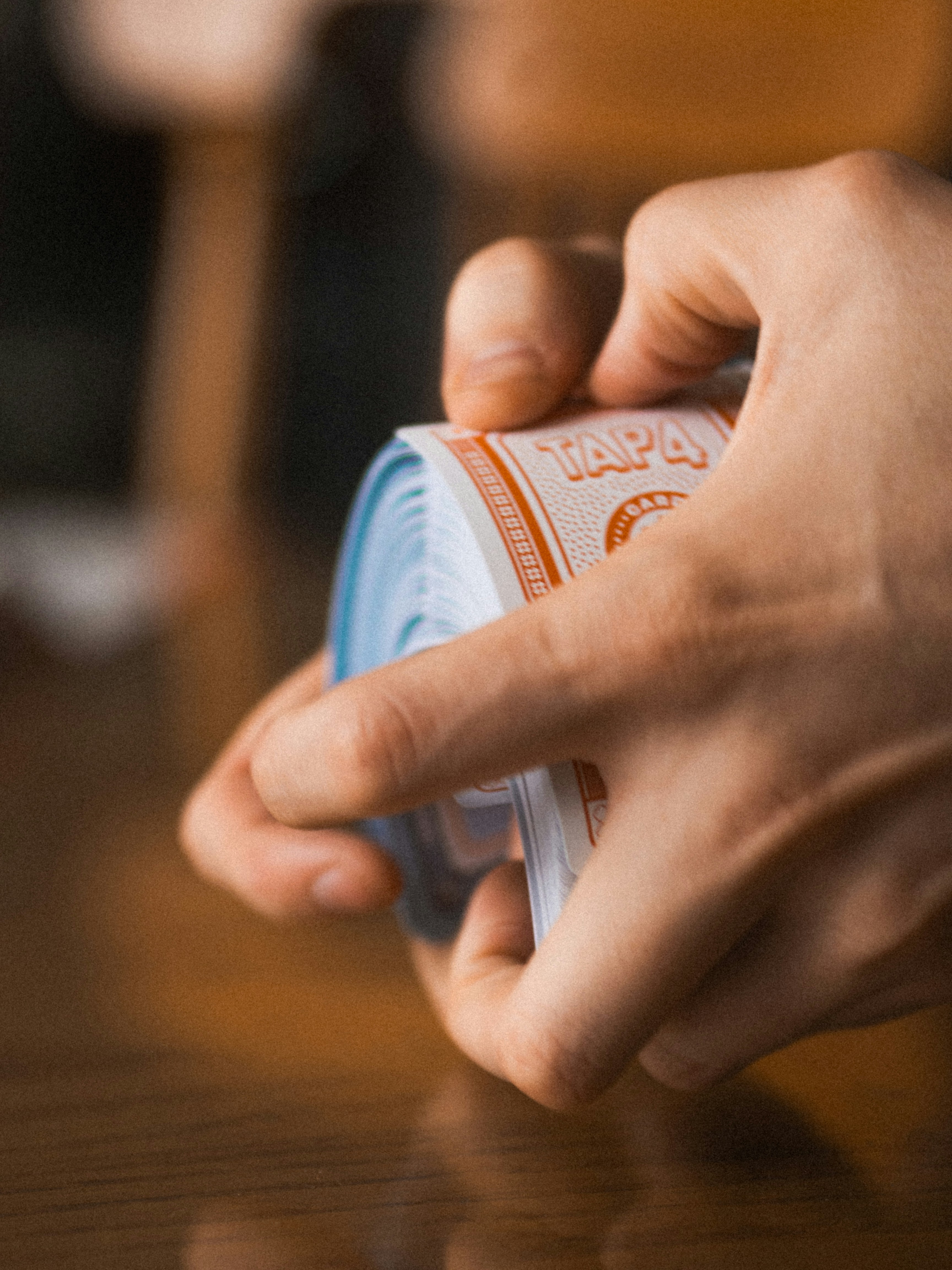 Close-up of hands gripping a roll of decorative tape, captured on a warm, wooden surface with soft bokeh in the background. A practical, intimate shot emphasizing texture and craft detail.