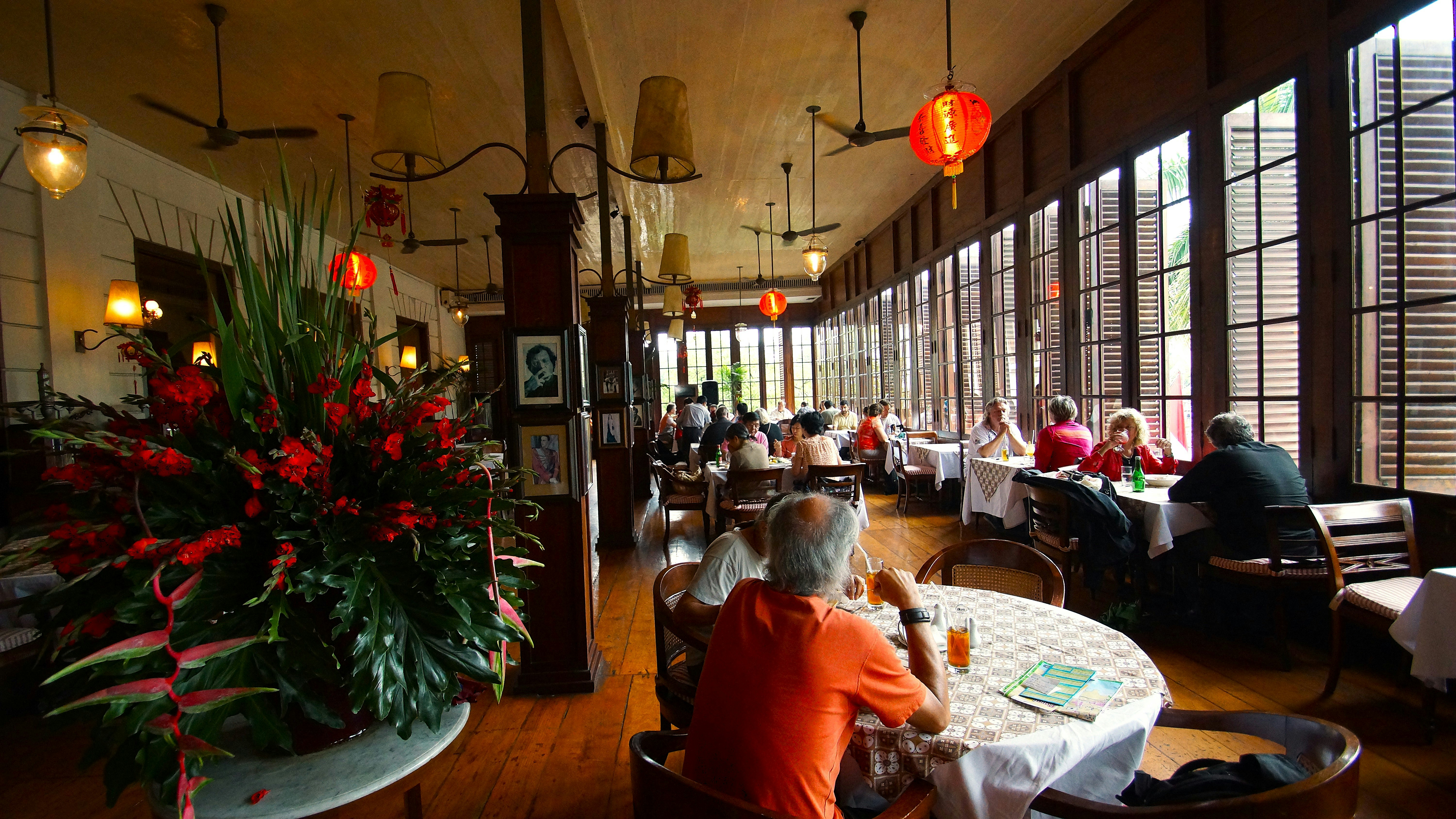Sunlit Bistro Pulse: People Dine Along a Glass-Walled Corridor