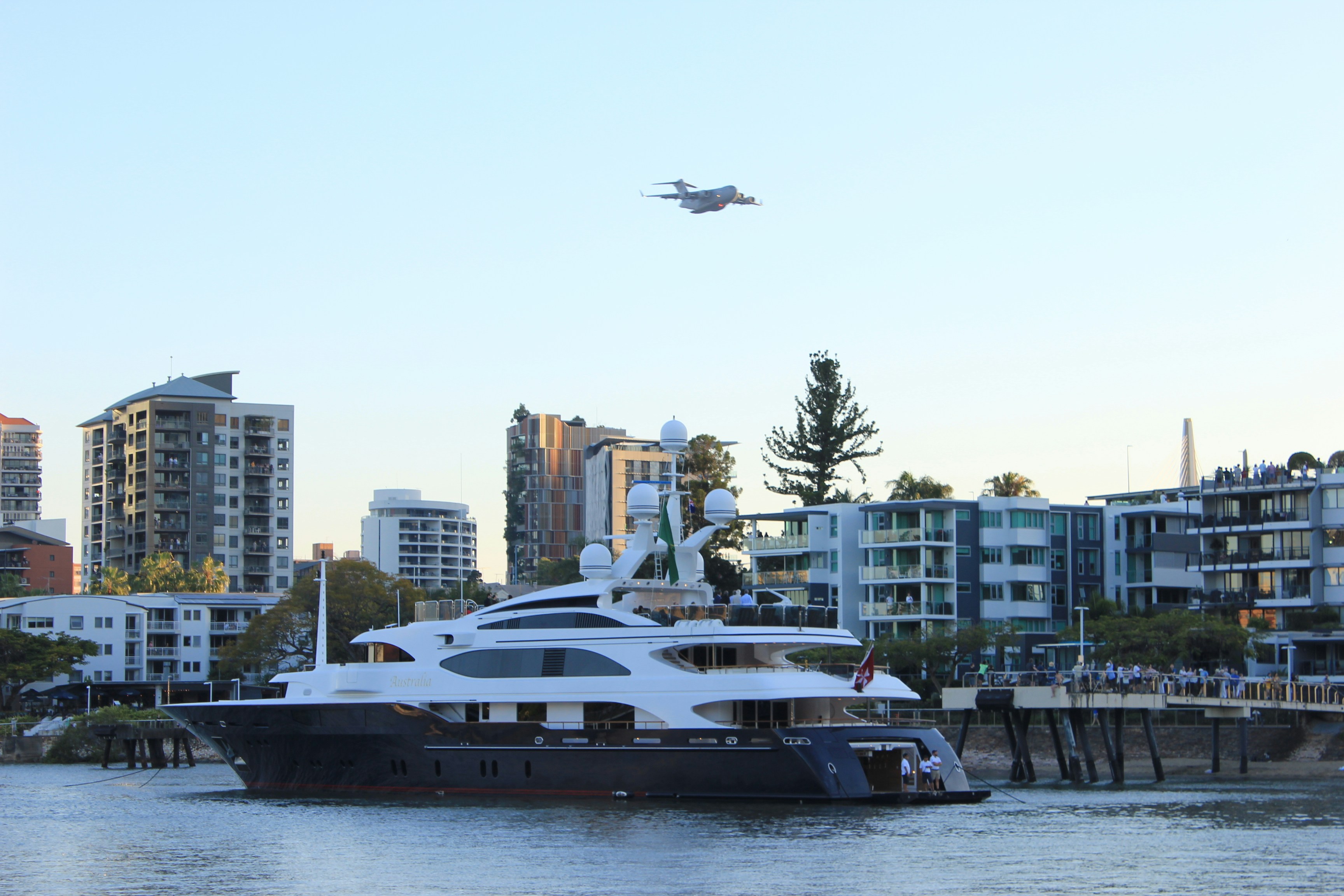 Yacht in calm harbor with helicopter overhead at golden hour