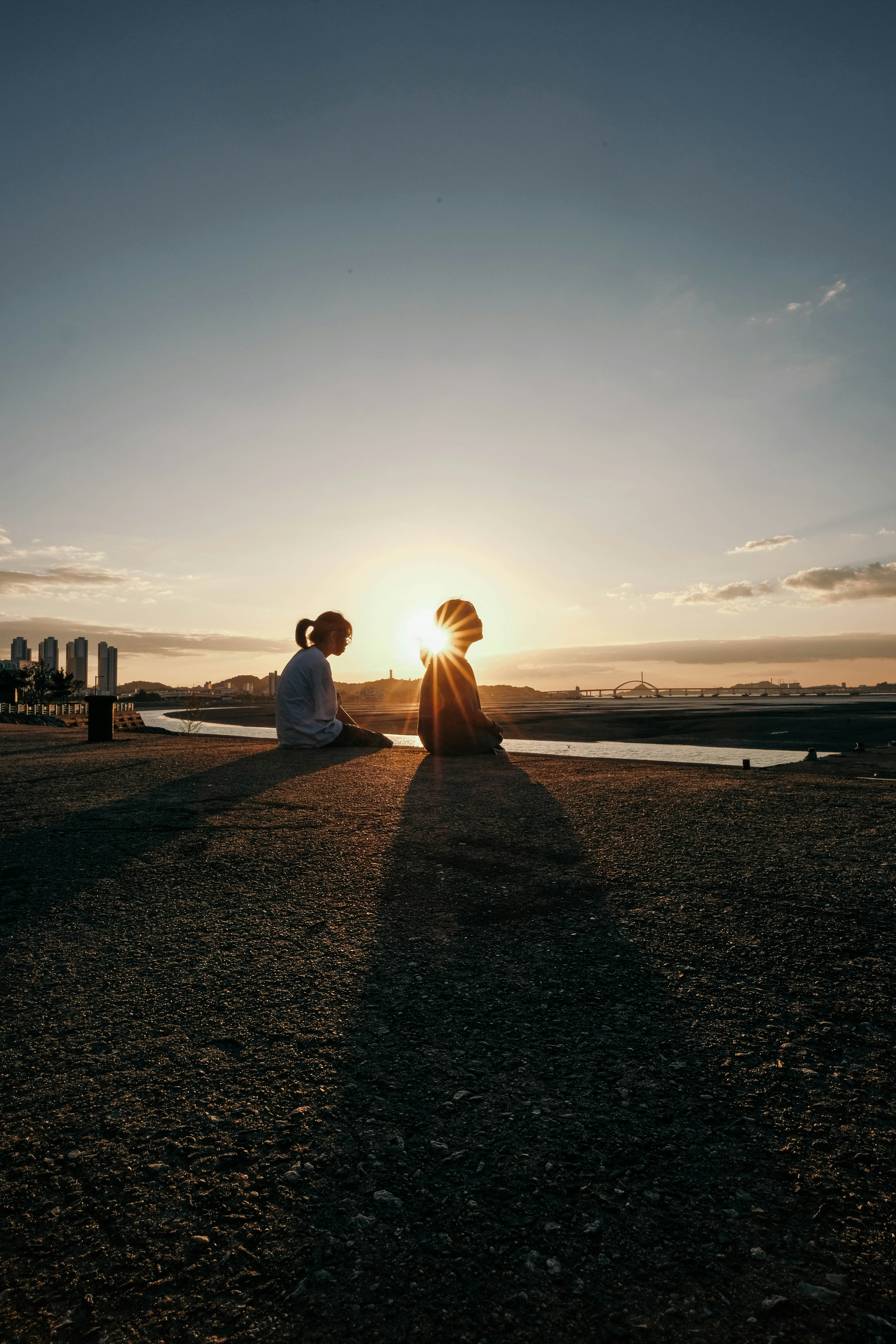 Sunlit Secrets: Two silhouettes share a quiet moment at the riverbank