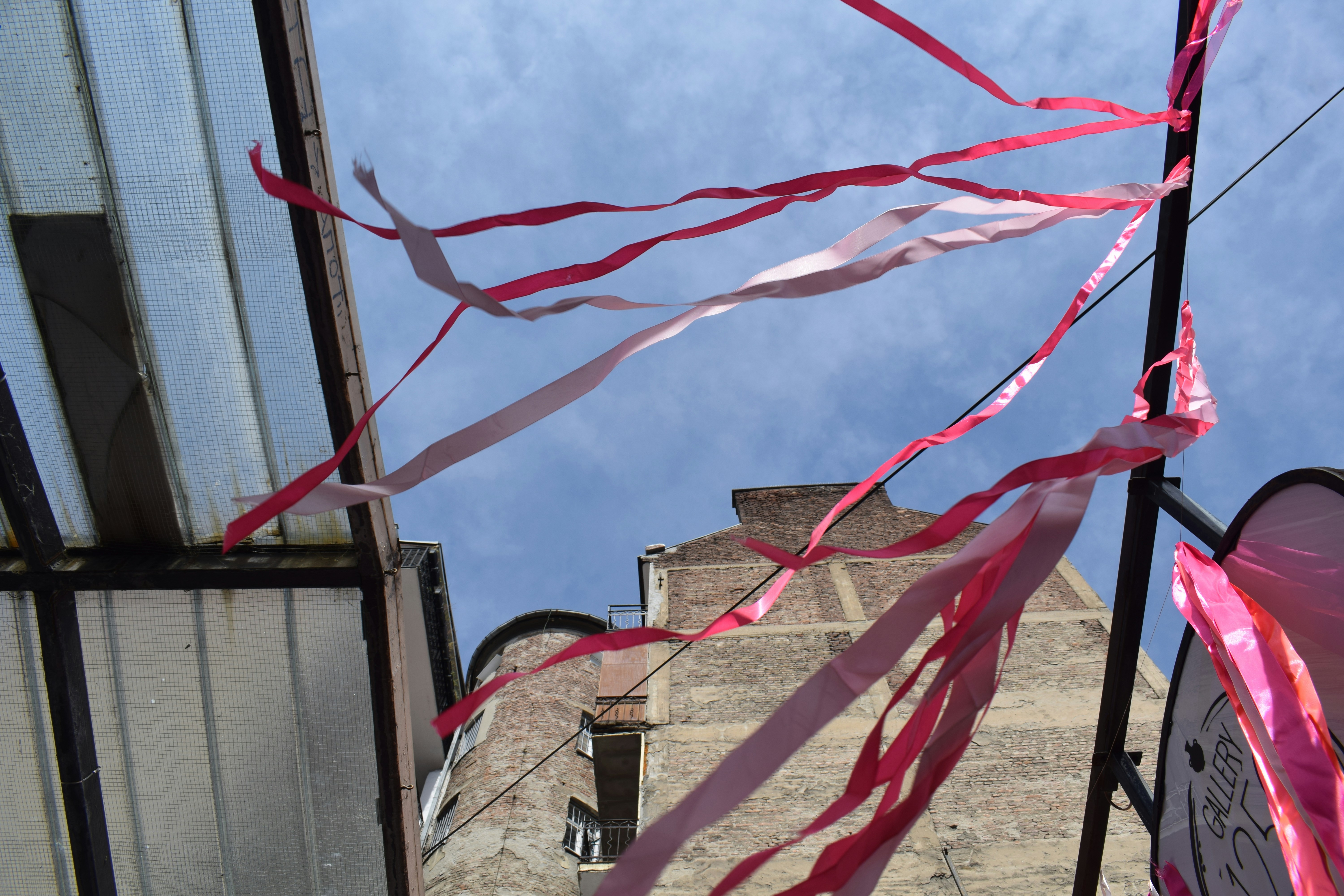 Ribbon Skyward Over Narrow Alley: Pink Strands Against Brick Facades