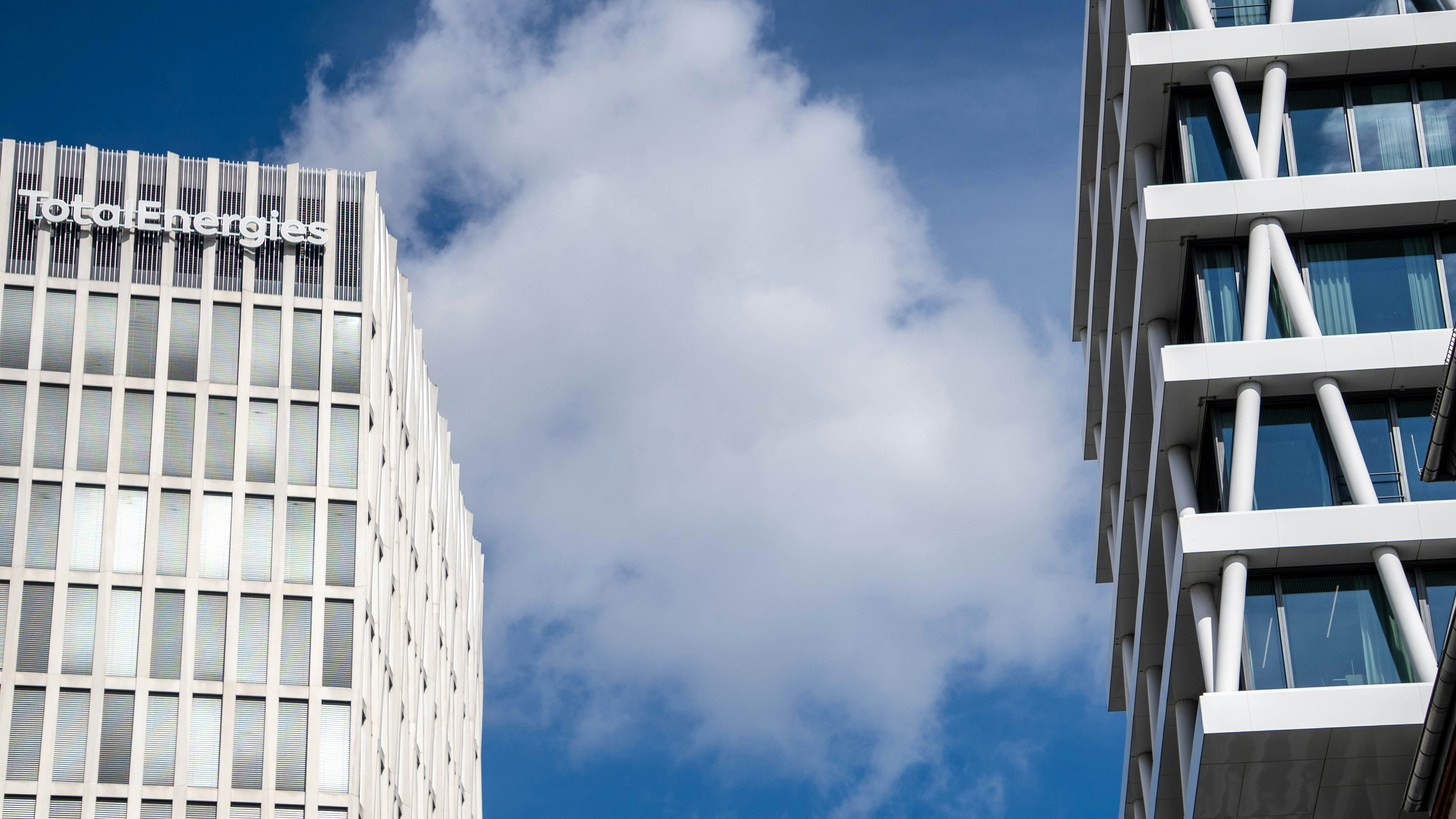 Two modern office towers frame a bright blue sky with a solitary cloud, emphasizing architectural geometry and vertical lines.