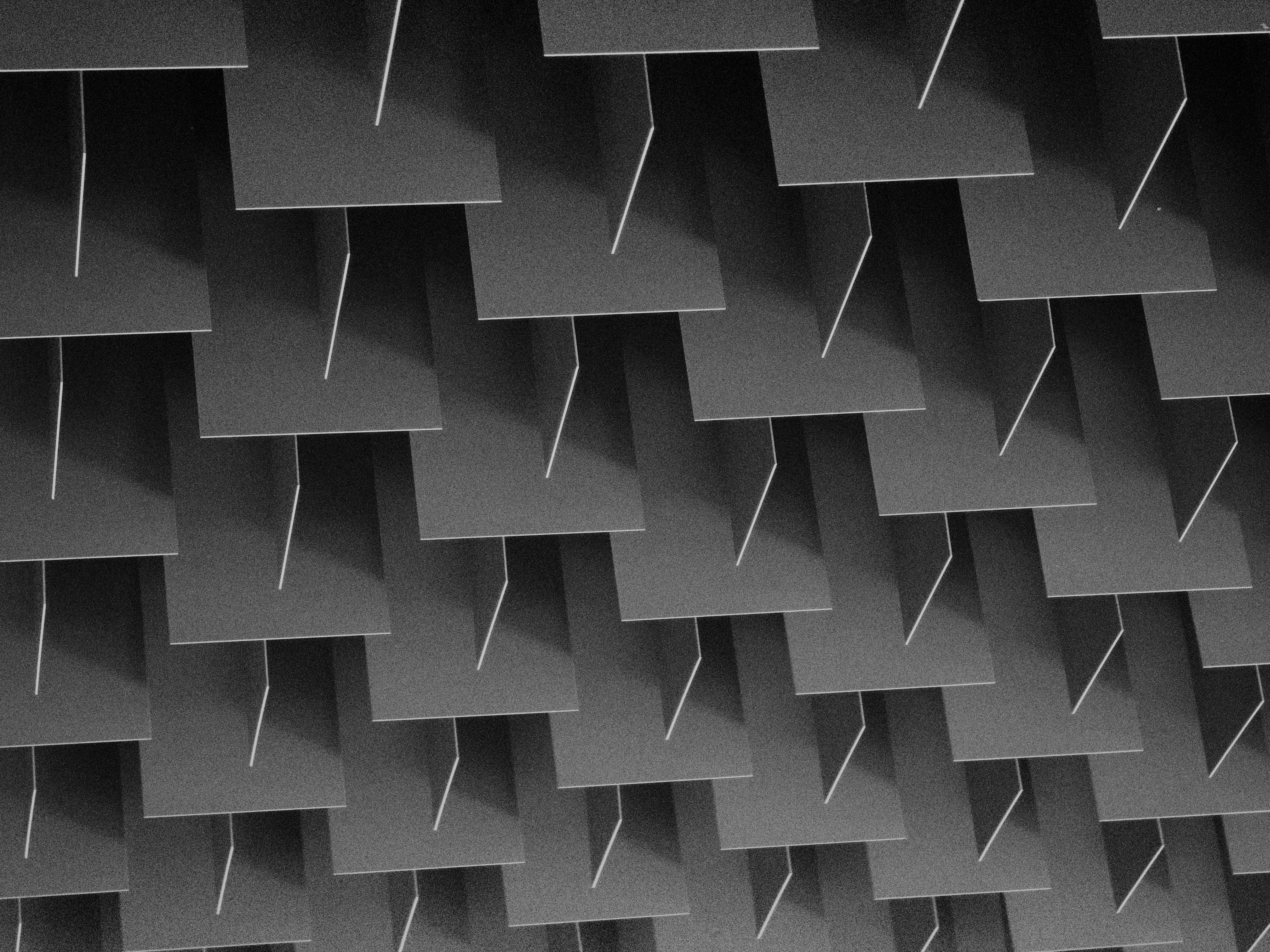 Monochrome wall composed of repeating angled panels creating a geometric, tessellated texture with subtle light and shadow variations.