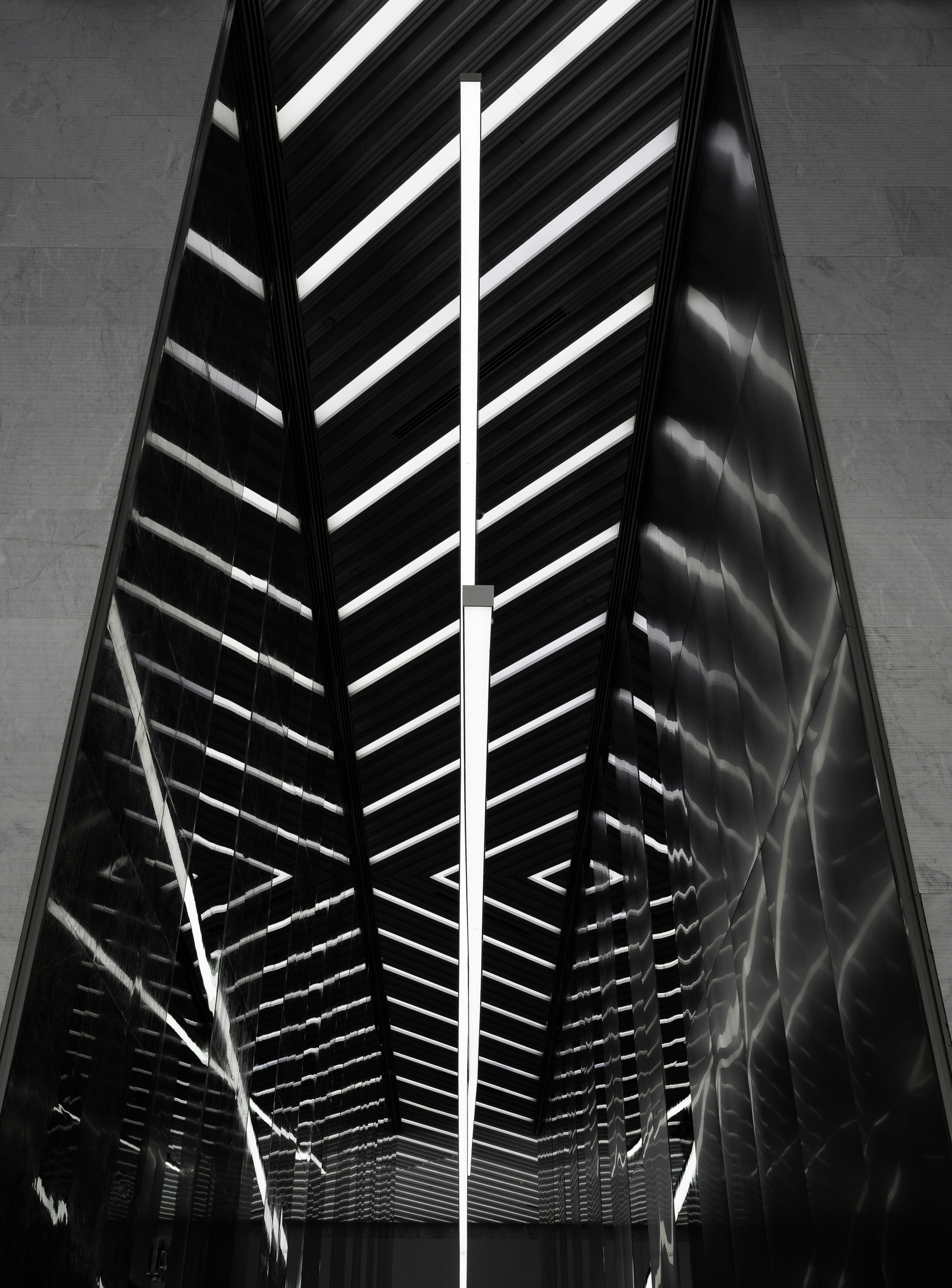 Monochrome interior of a modern stairwell or corridor with dramatic vertical light bars creating a geometric rhythm and infinite perspective. A logo-free architectural shot emphasizing symmetry and line work.