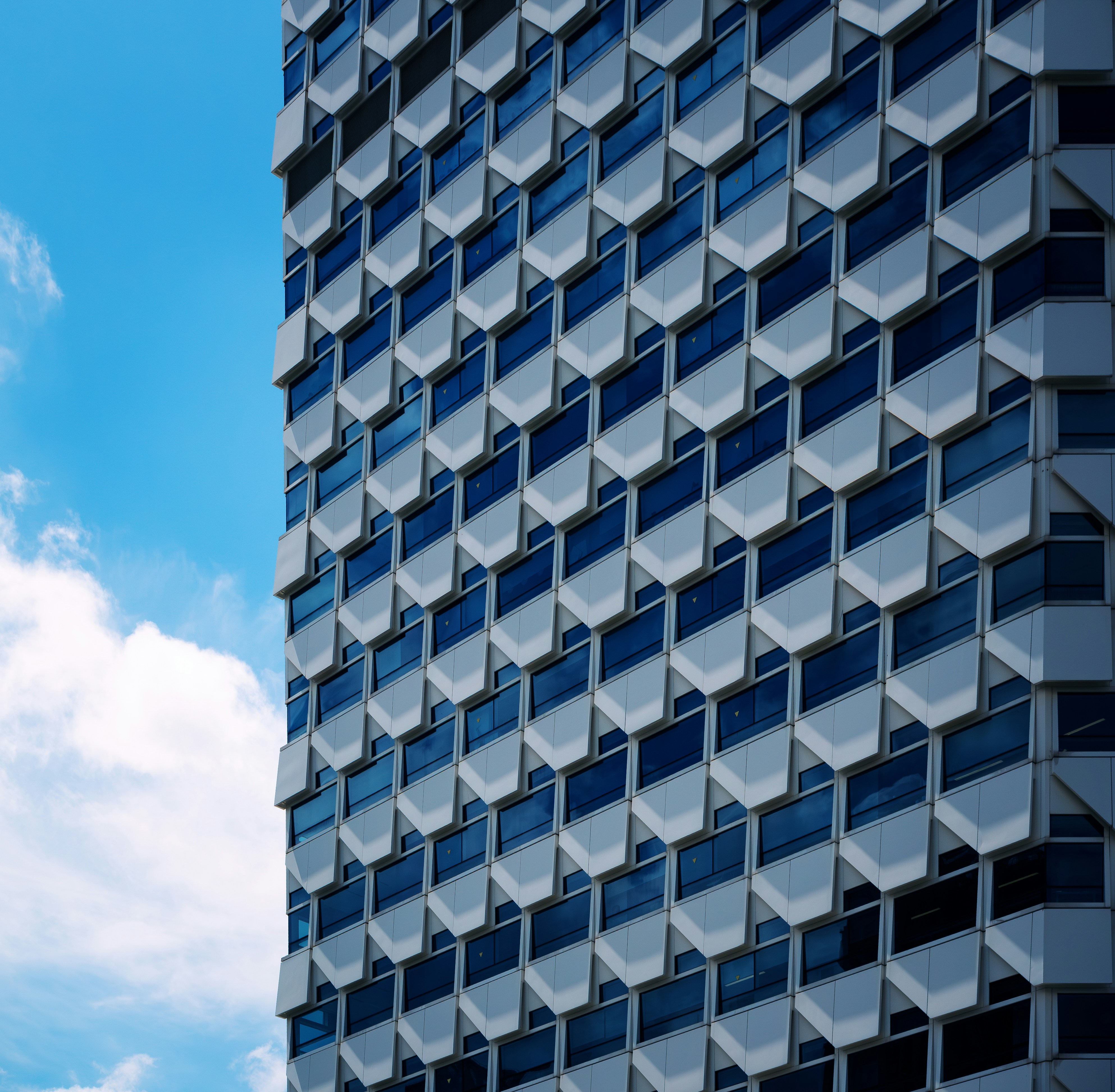 Checker-patterned office façade with diagonal protrusions against a blue sky and white clouds.