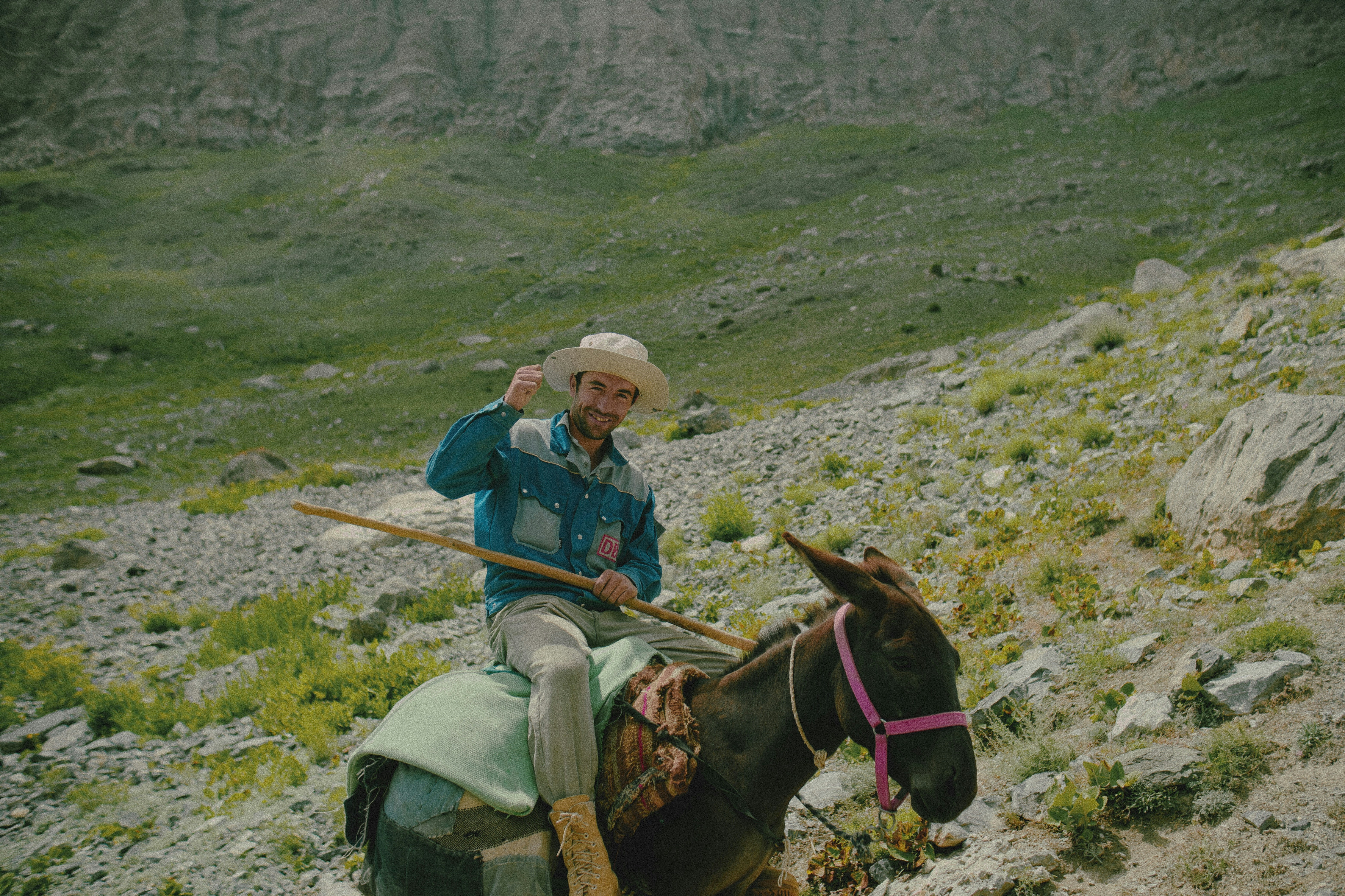 Rider in a turquoise shirt Guides a Horse Across a Rocky Highland