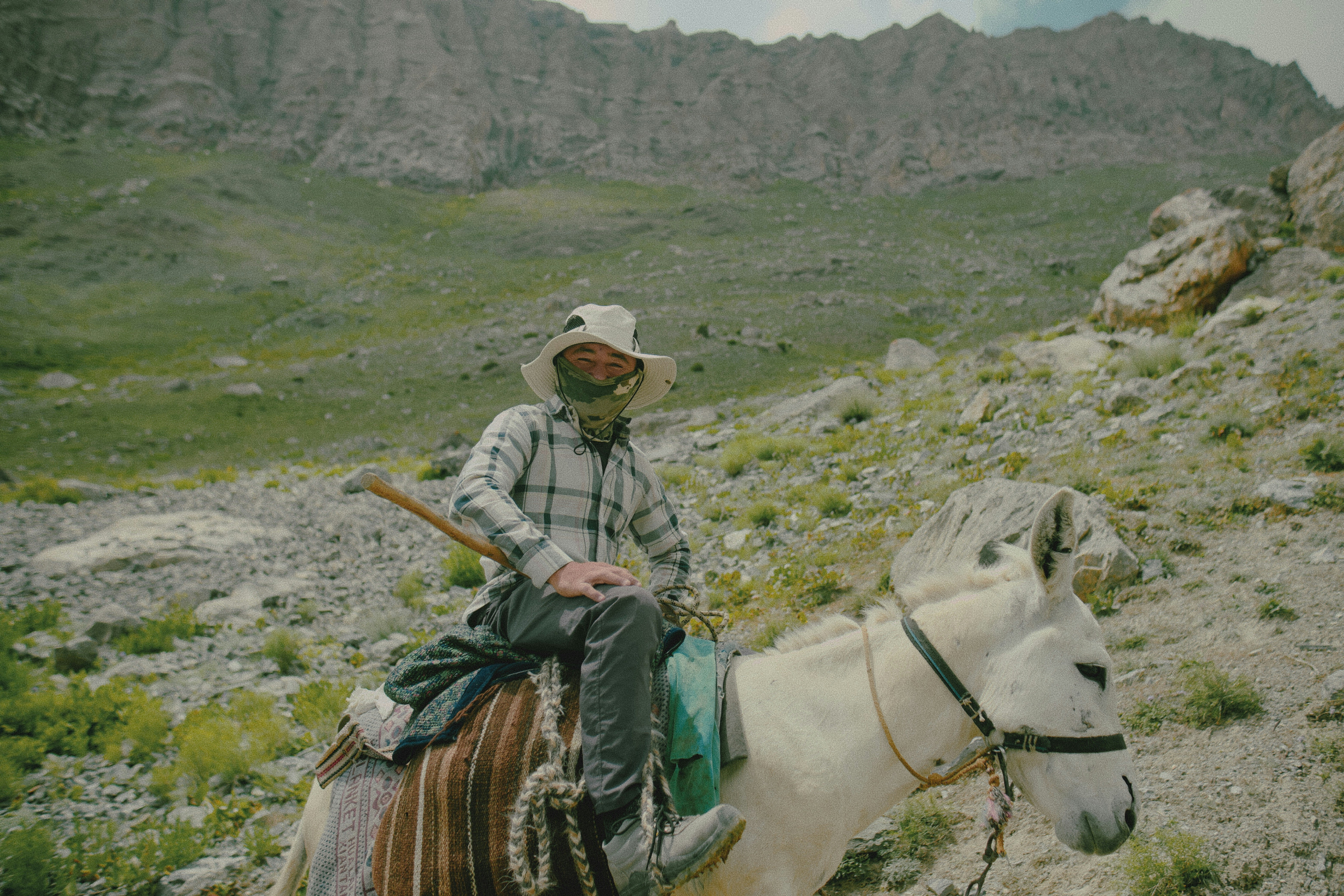 Rider and white horse traversing a rugged alpine landscape