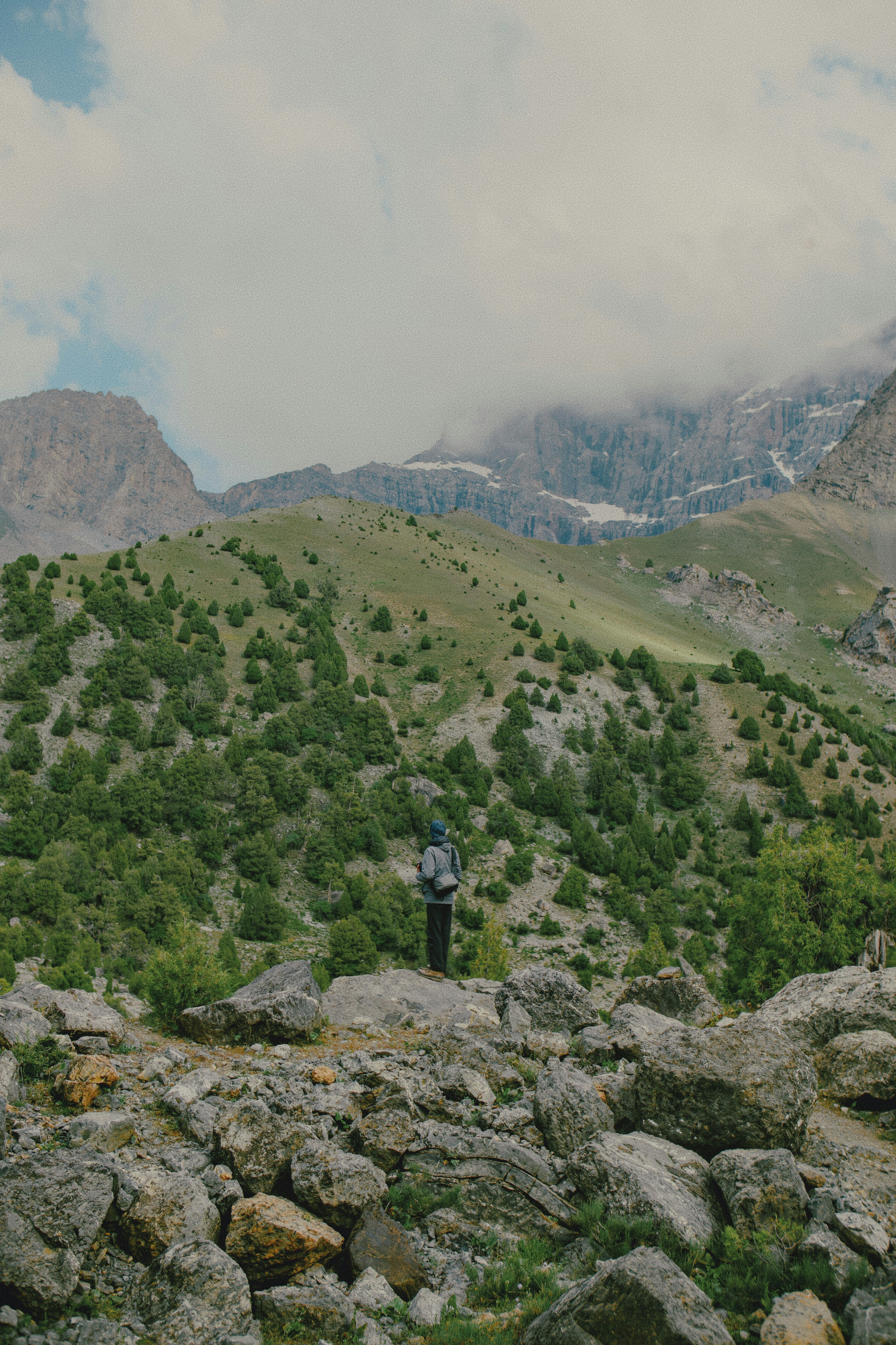 Hiker Amidst Marshaled Rocks Under Alpine Clouds