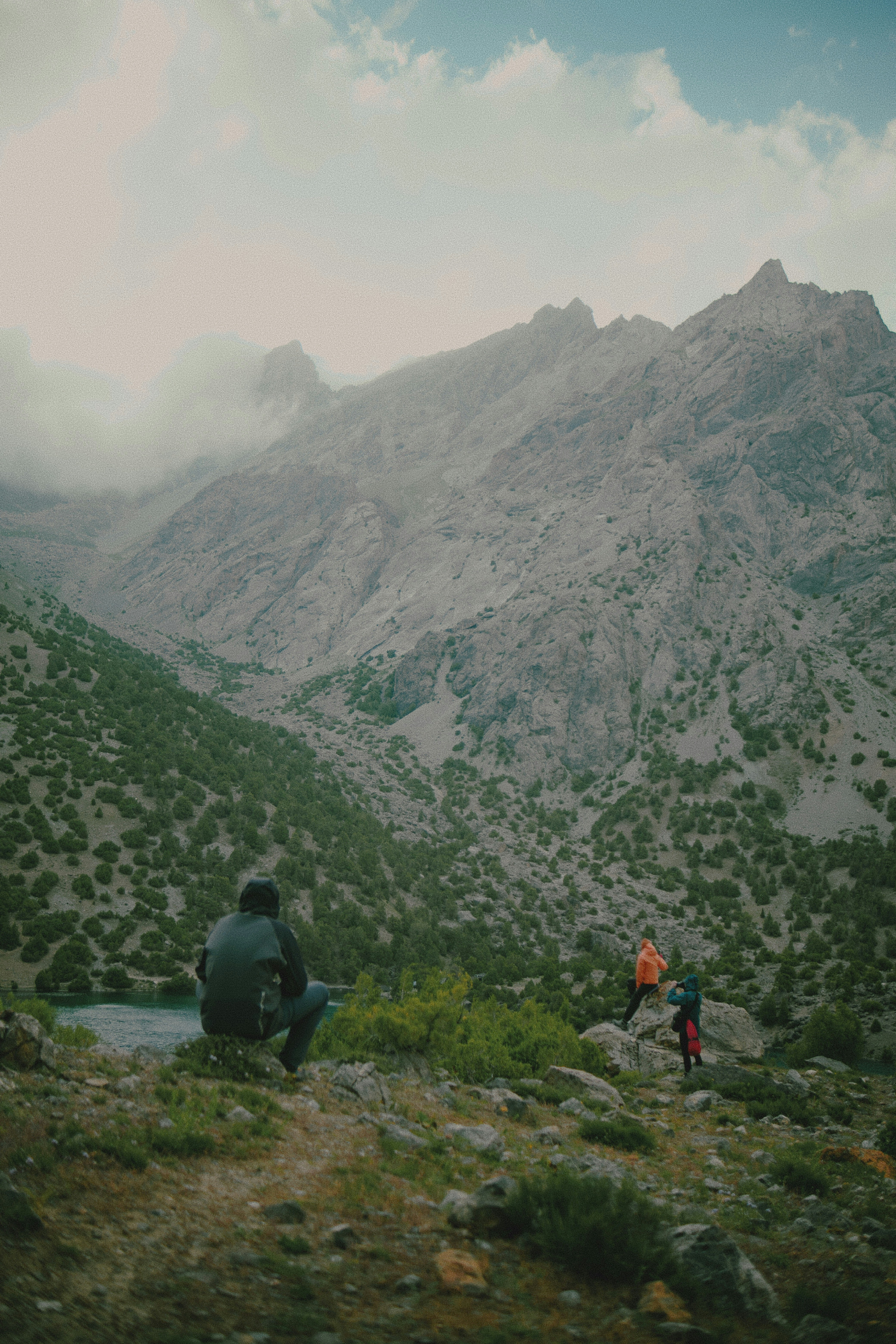 Three people on a rocky slope overlooking a mountain lake and forested valley