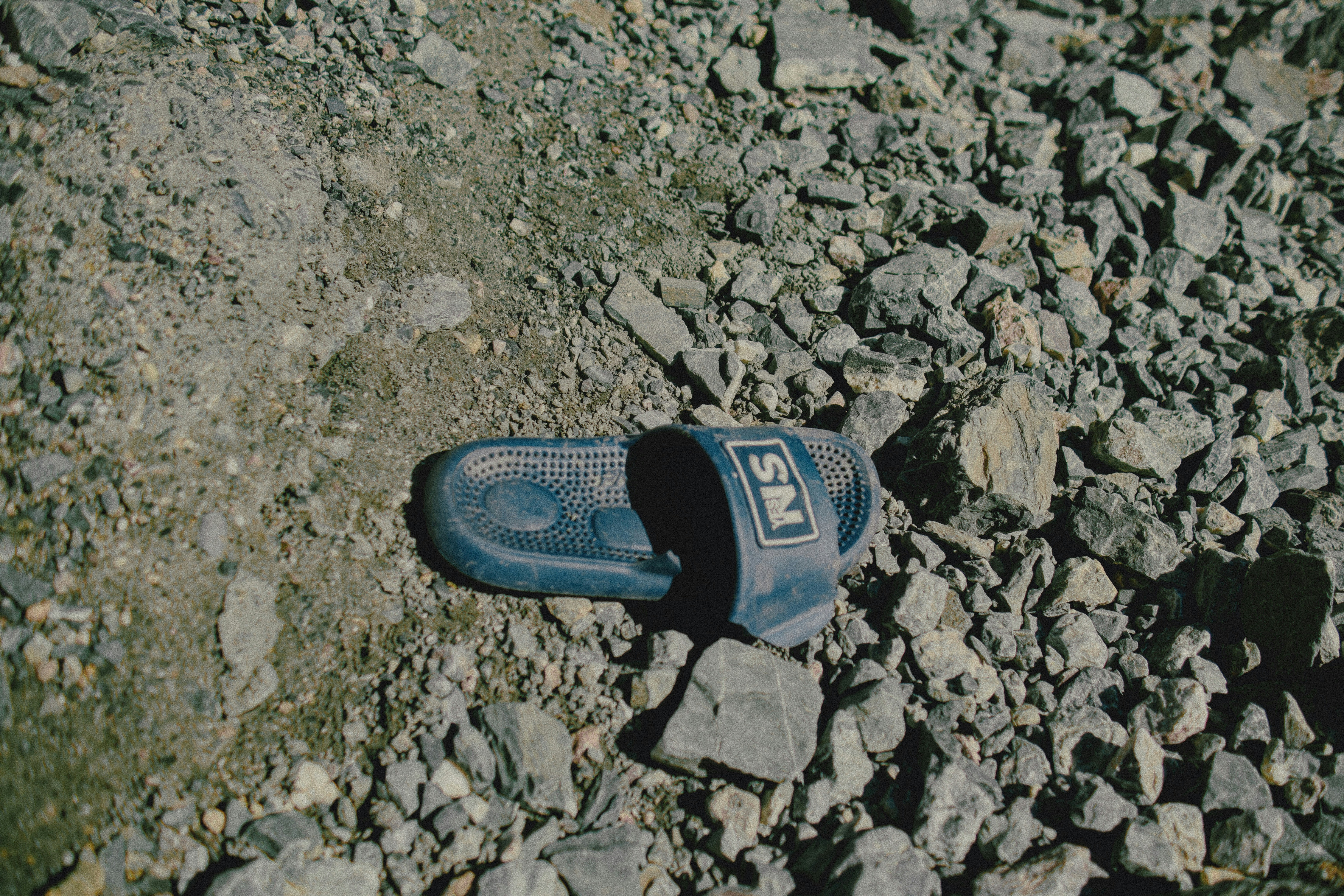 Blue Slip-On on Gravel: A Moment of Quiet on the Shoreline