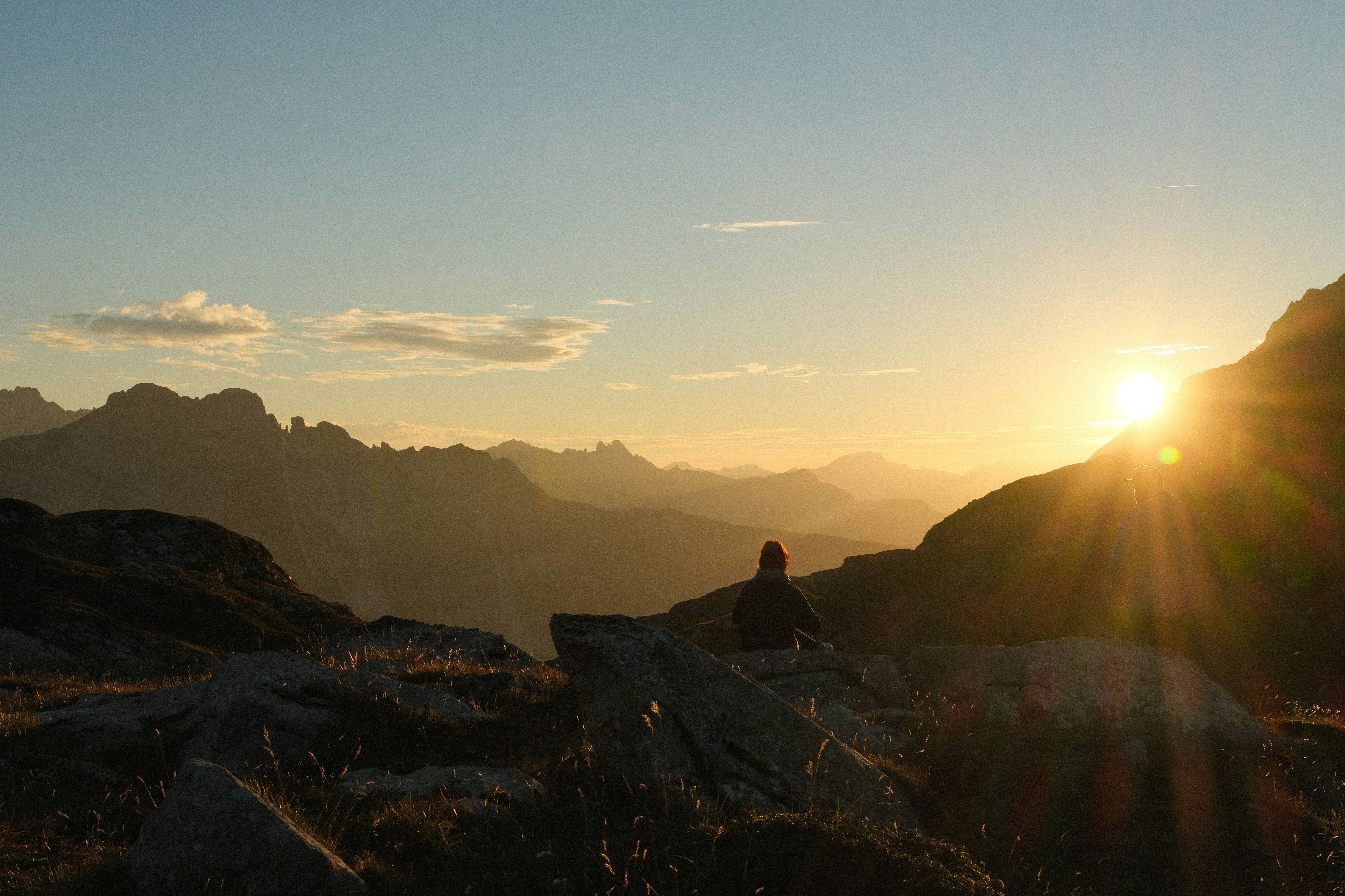 Sunlit Solitude: A Lone Figure Amid Mountain Silhouettes at Dawn