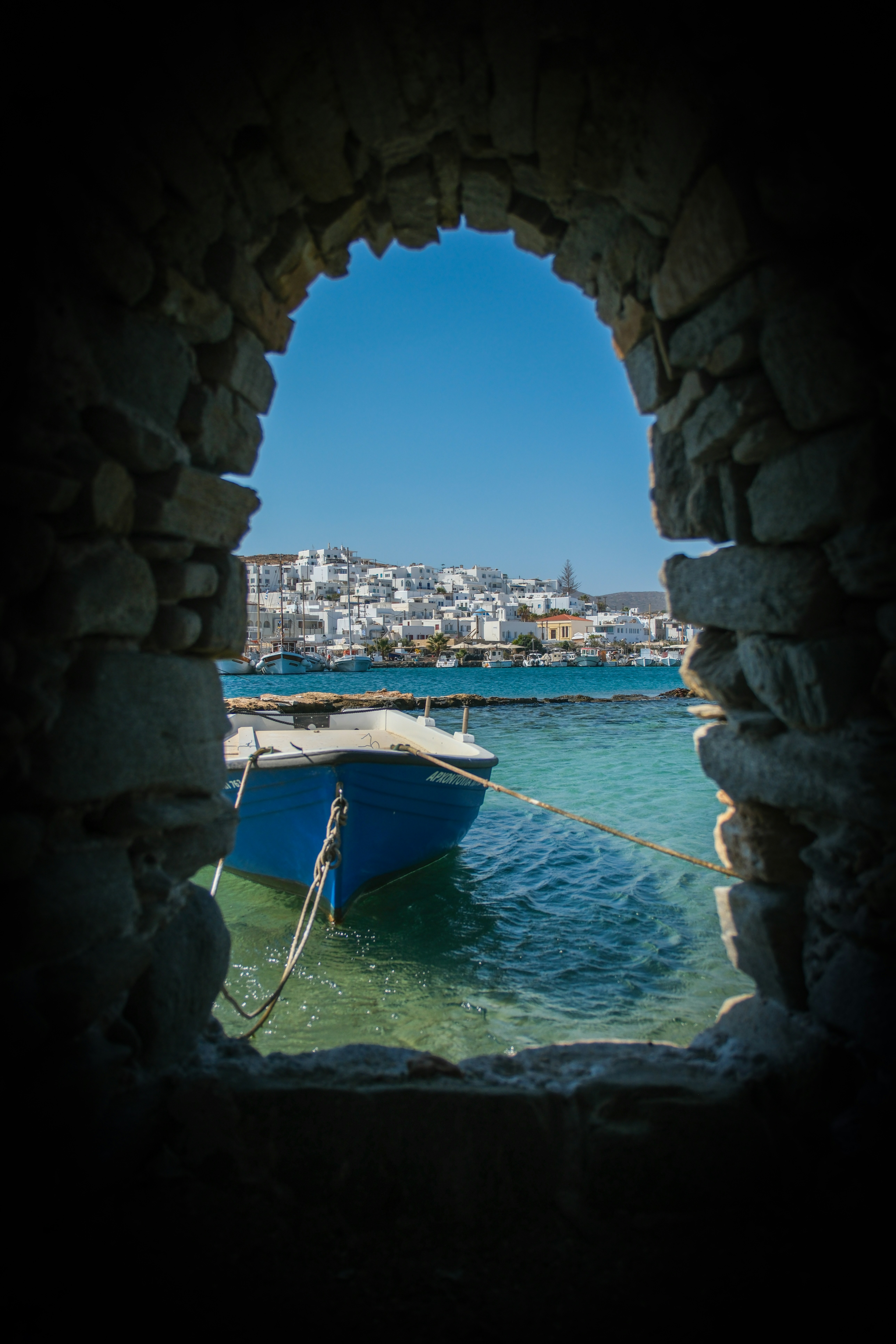 A blue boat moored in clear water viewed through a stone archway