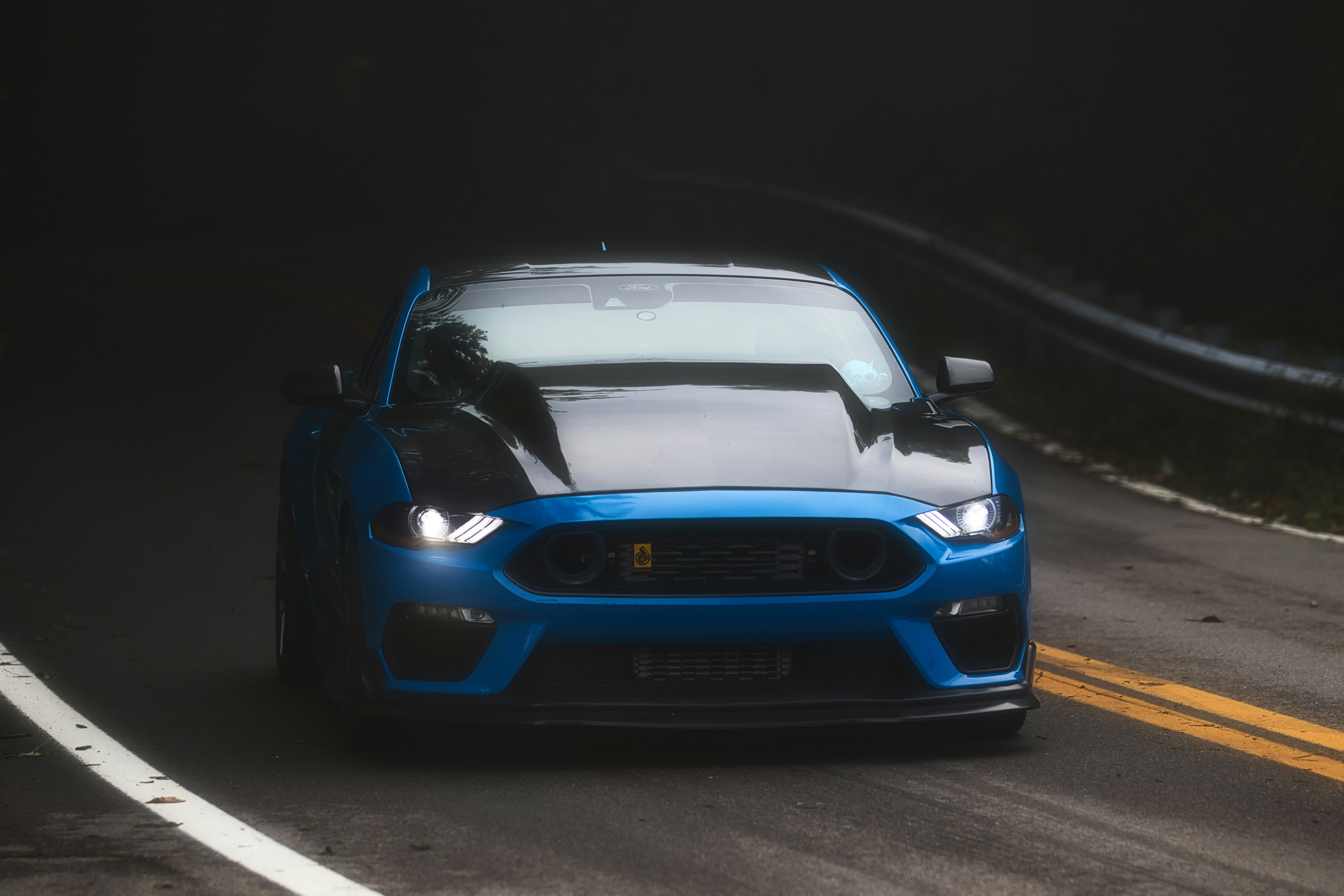 Blue sports car blasting through a winding road, lens flare and motion implied by slight blur and dust in the frame.