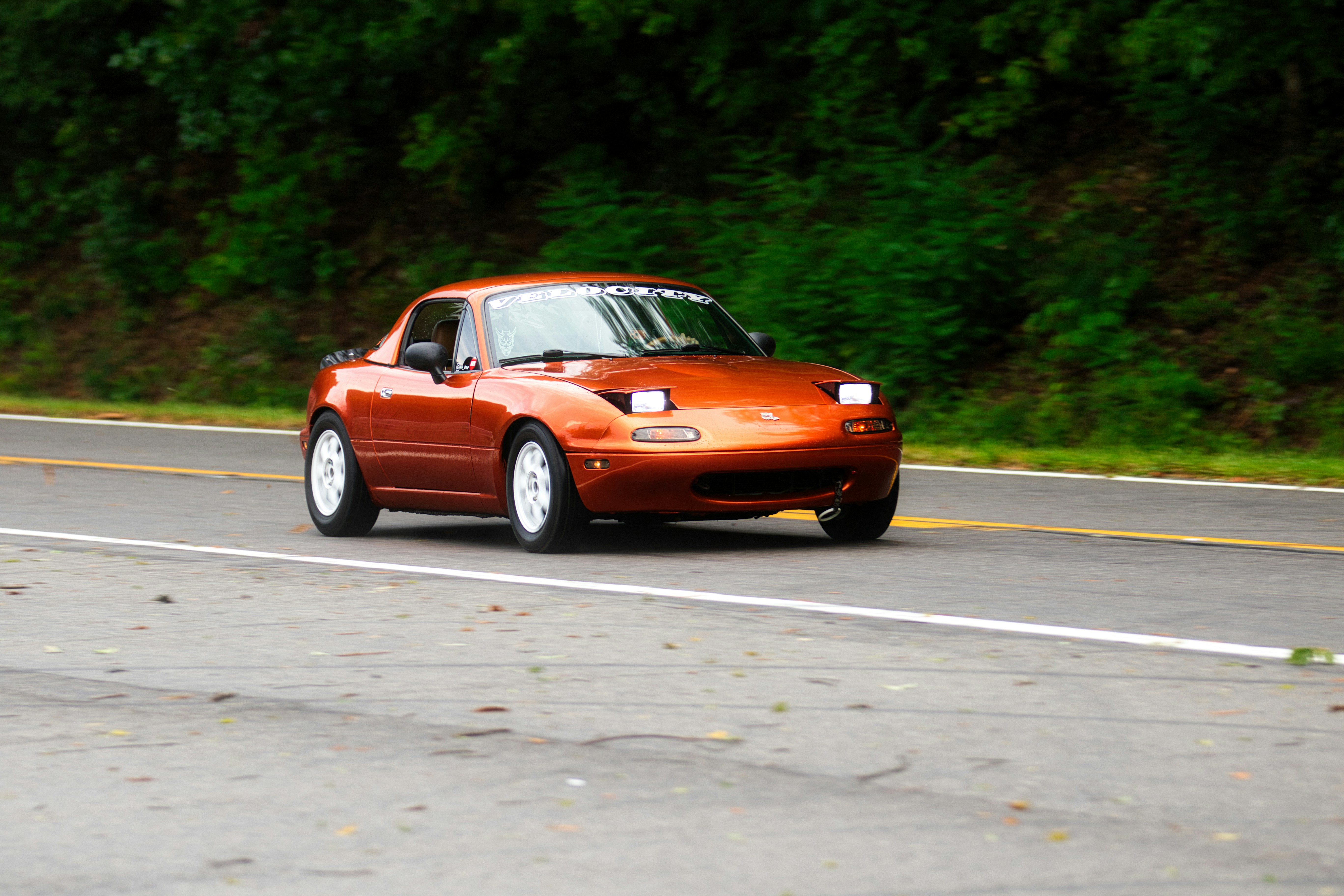 Orange coupe in motion along a tree-lined highway