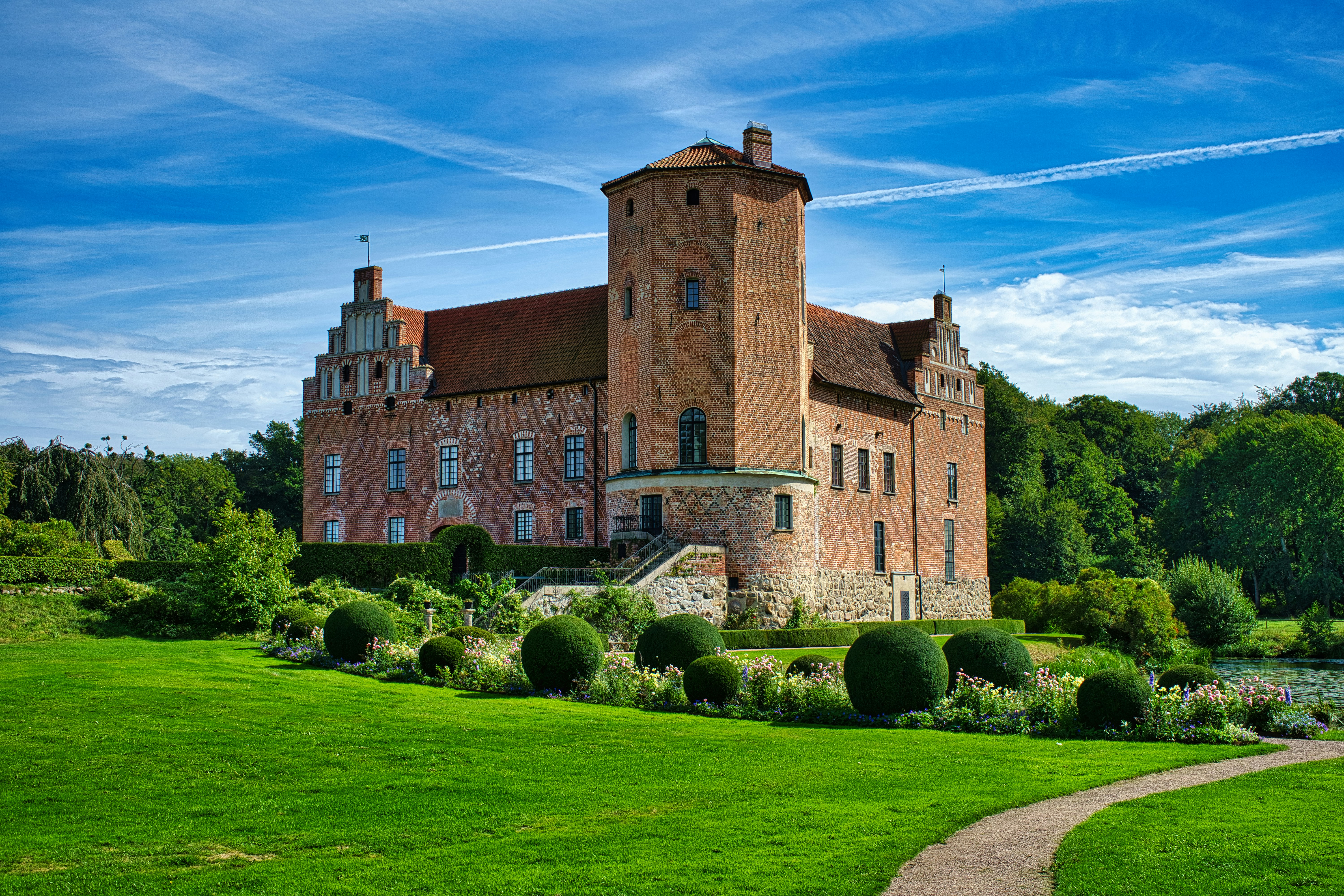 Sunlit Brick Castle Surrounded by Pruned Gardens and Rolling Green