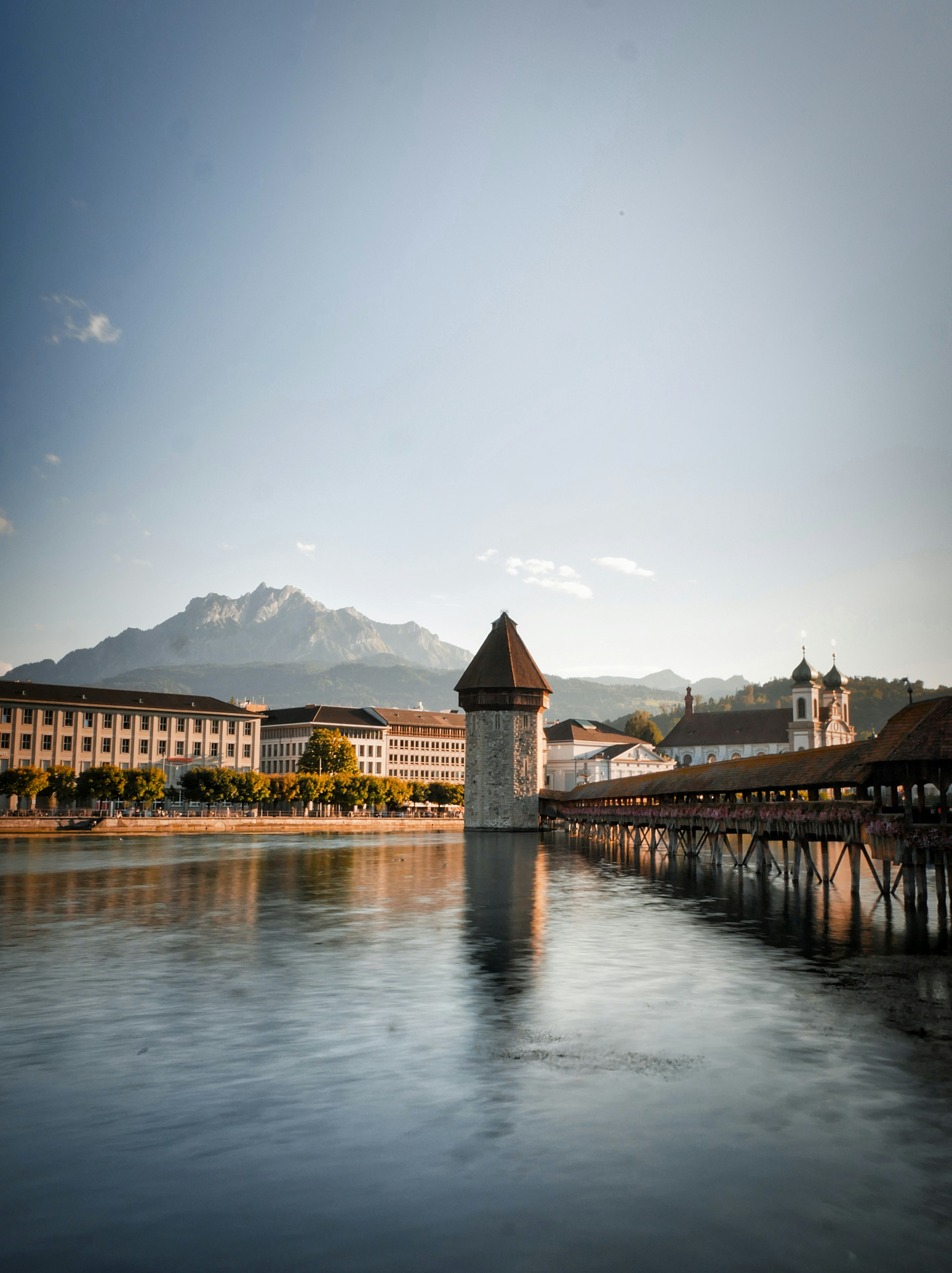 Bridge and tower resting on a tranquil alpine lake with distant mountains