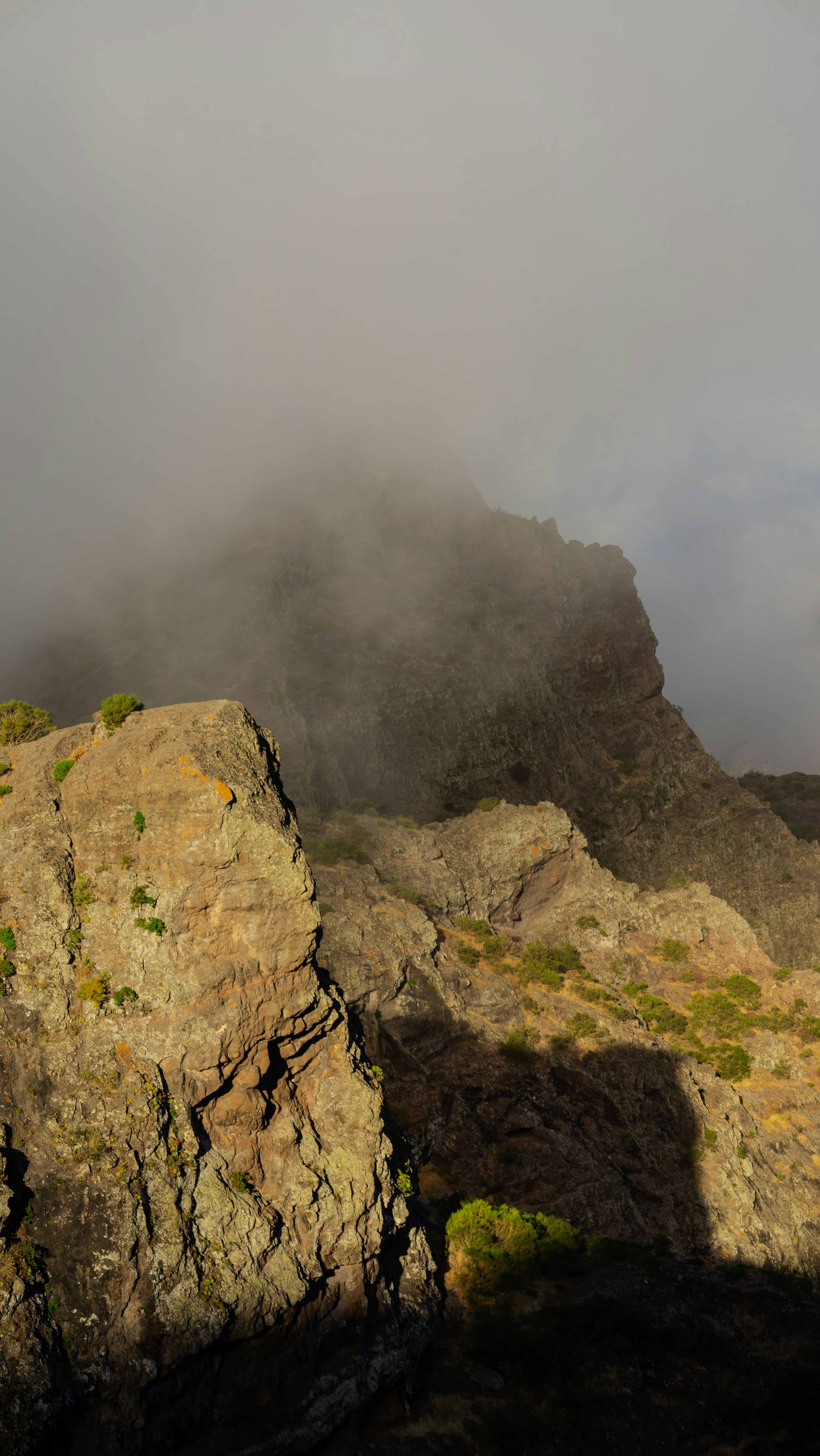 Mist on the Ridge: Sunlit Cliff Beneath Shrouded Peaks