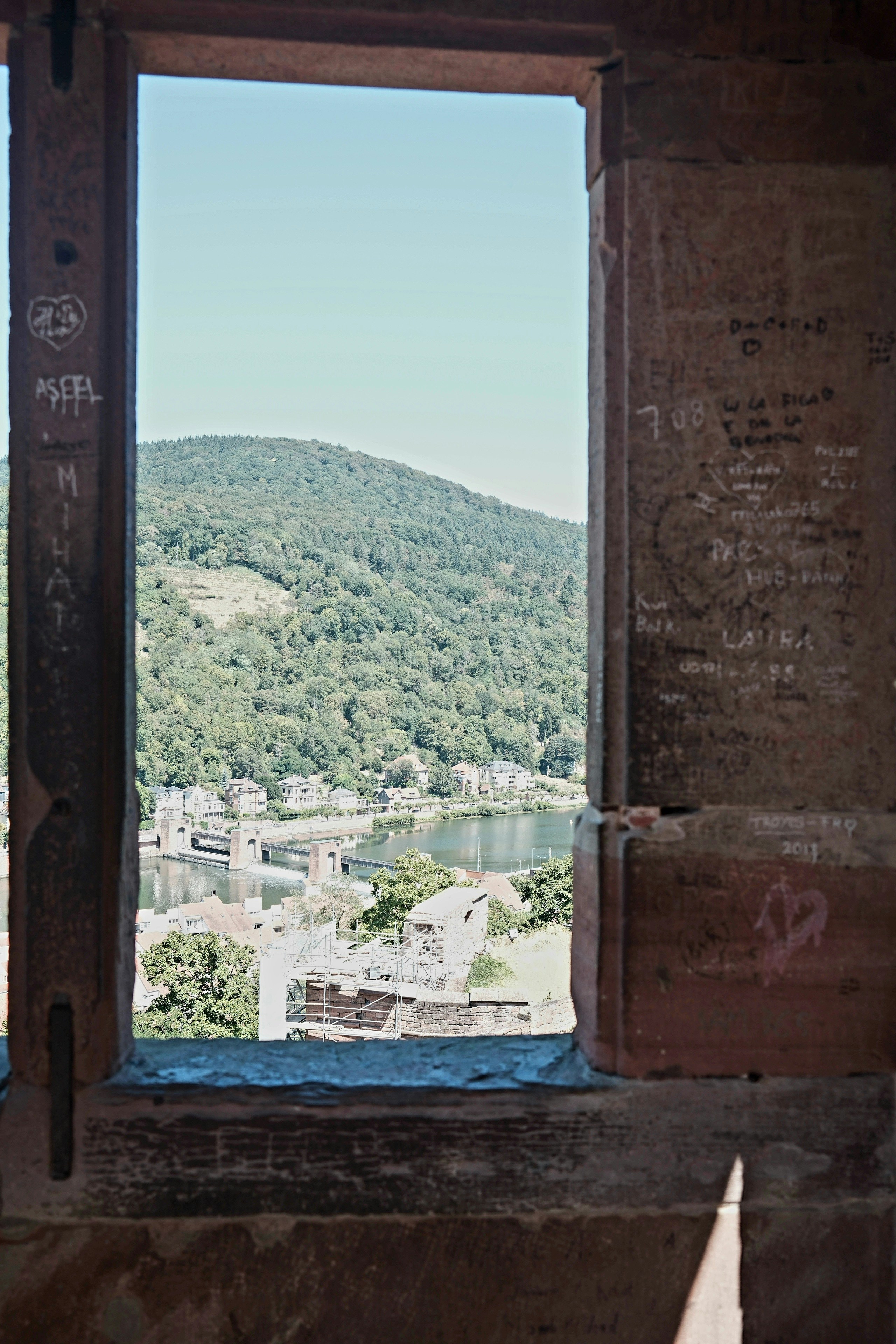 View through a weathered window: hillside village and river framed by stone walls
