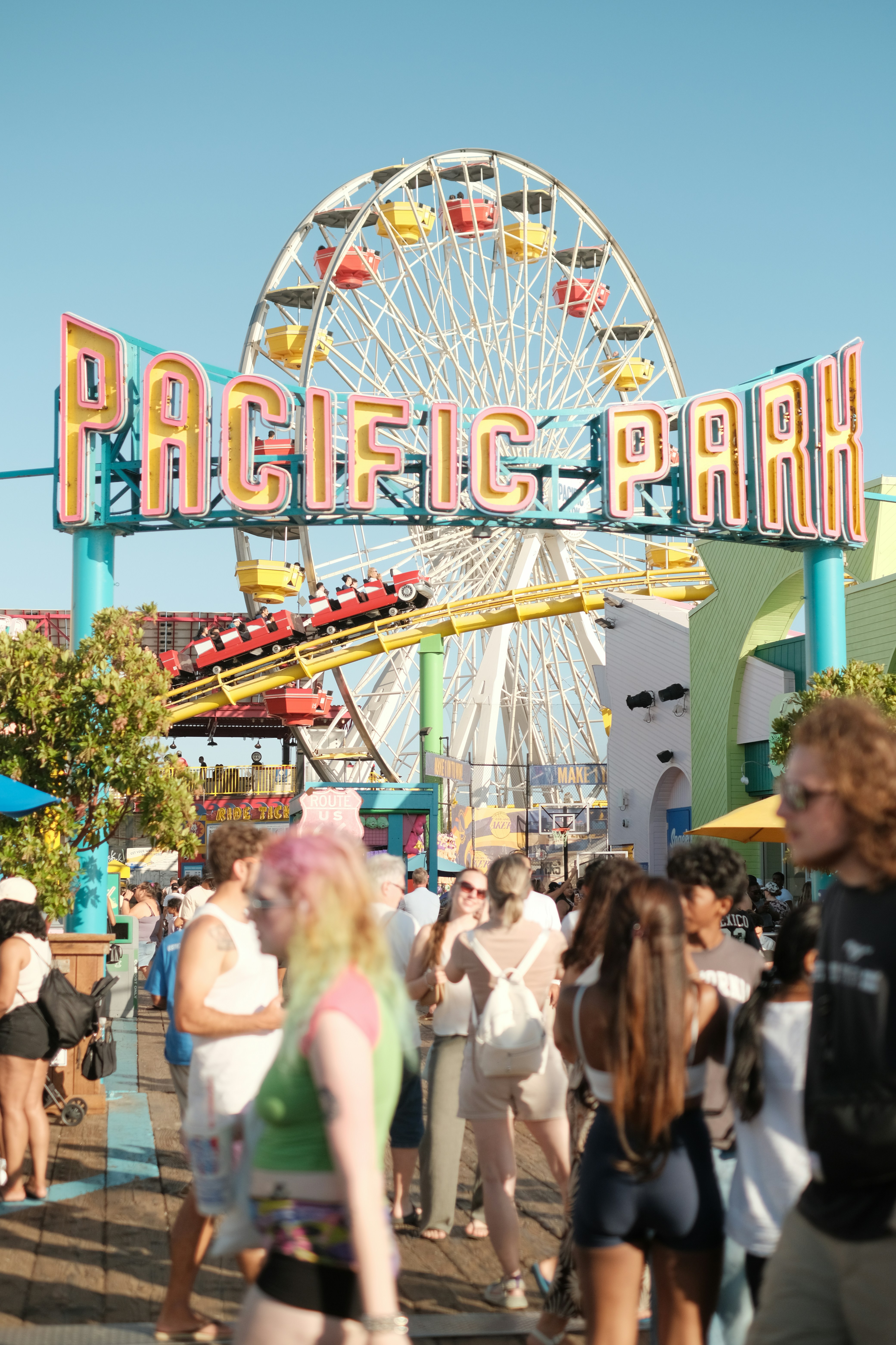 Neon Gateway at Pacific Park: A Ferris Wheel rises above a sunlit crowd