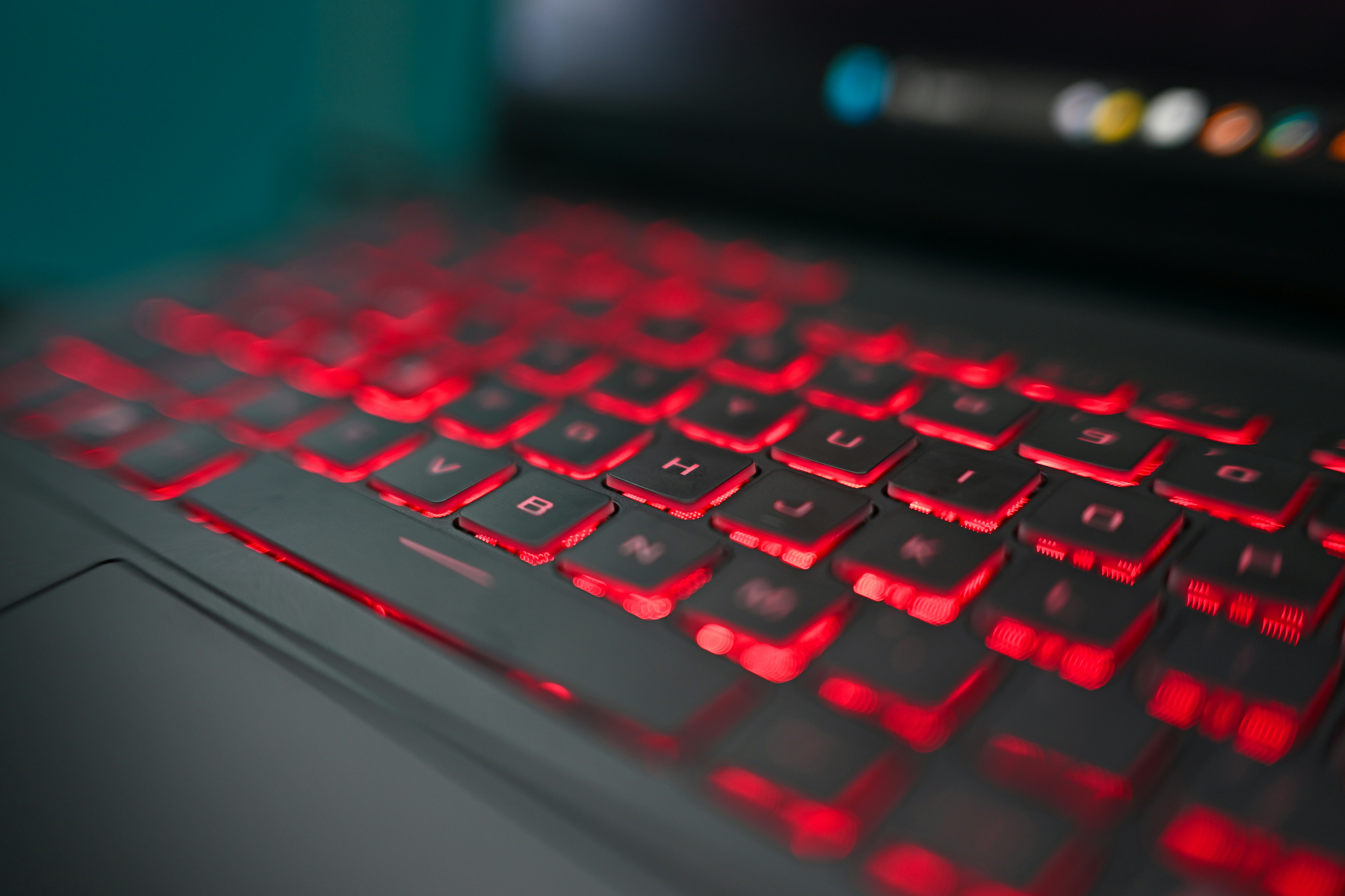 Glowing red backlit keyboard on a dark laptop, captured with a shallow depth of field to emphasize the illuminated keys and soft bokeh in the background.