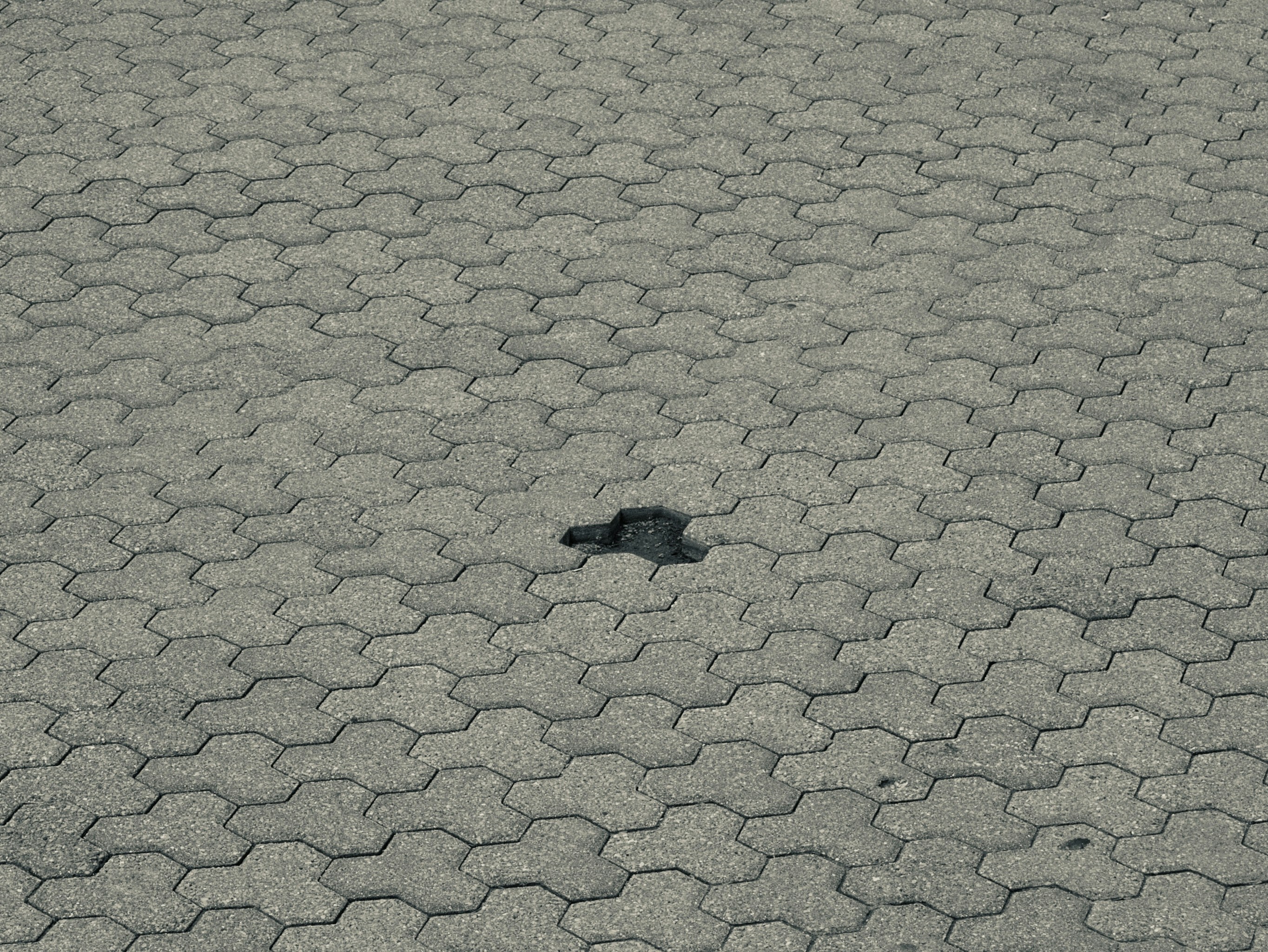 Close-up of a textured, hexagonal cobblestone pavement with a small dark irregular chip near center; emphasizes surface detail and subtle imperfections.