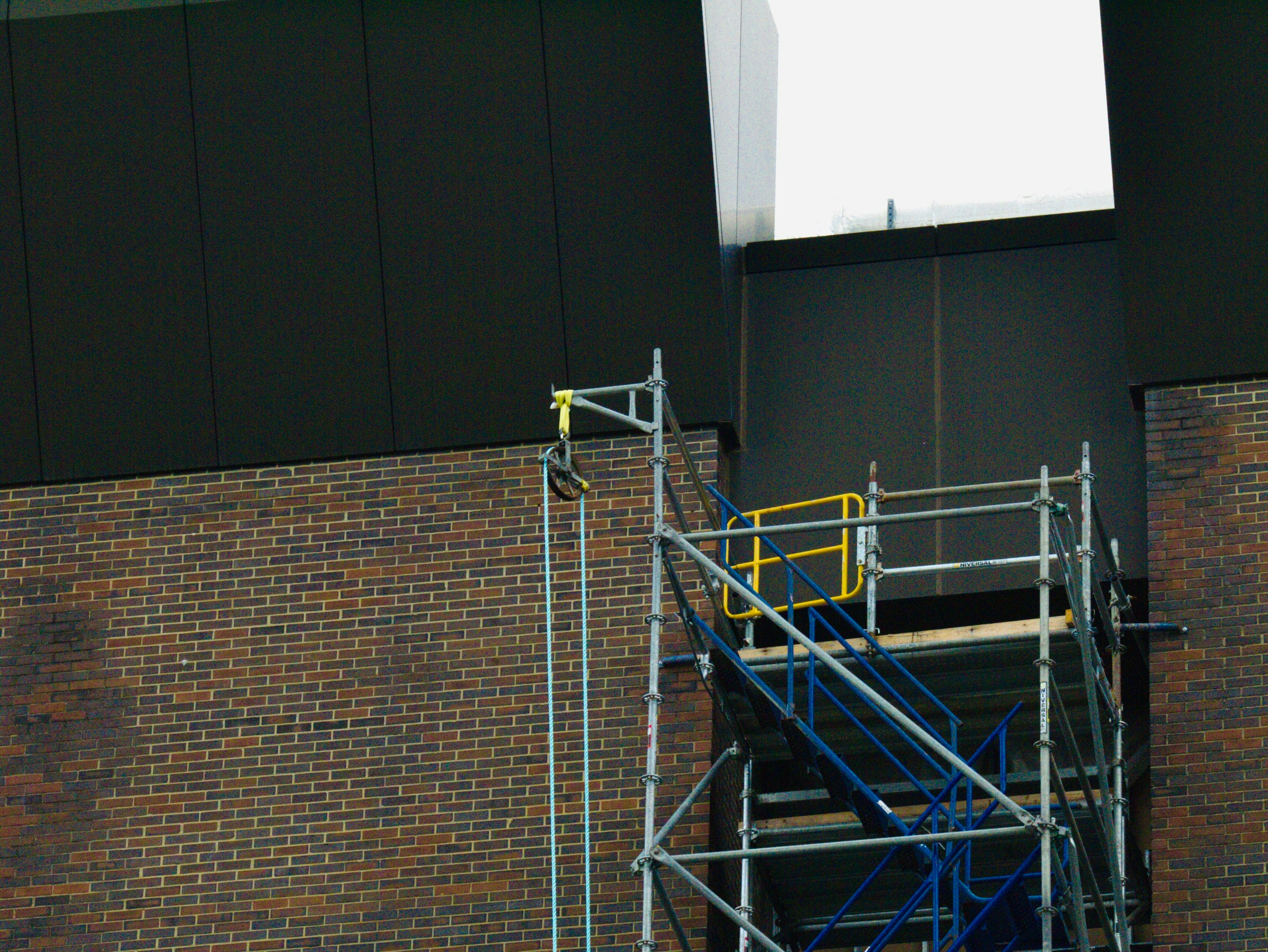Scaffolding against a brick wall with a small opening above, suggesting an active construction site.