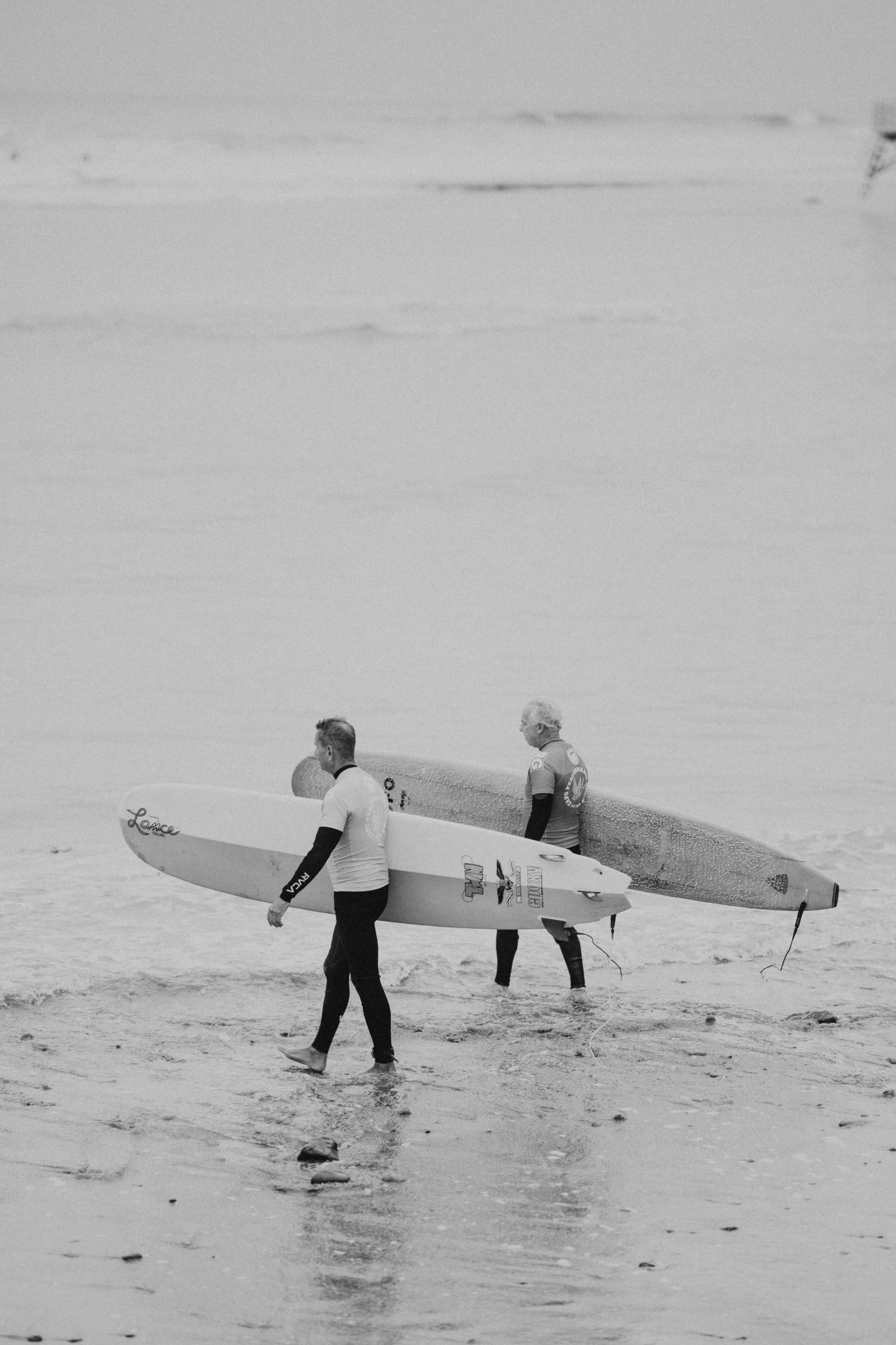 Two Surfers Stepping from Tidal Shore with Boards in Tow