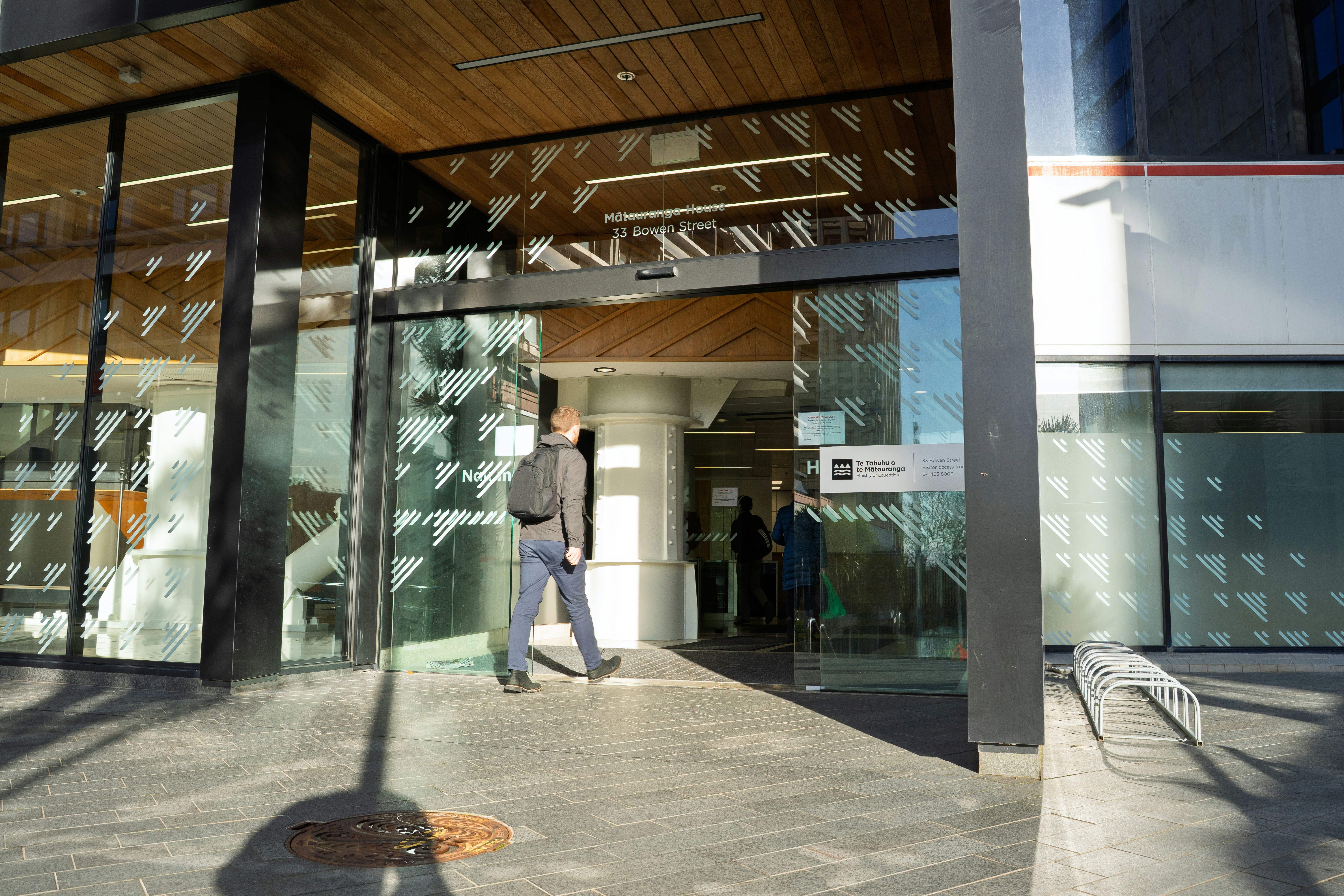 Glass doors, shadows, and a lone traveler at a modern office facade