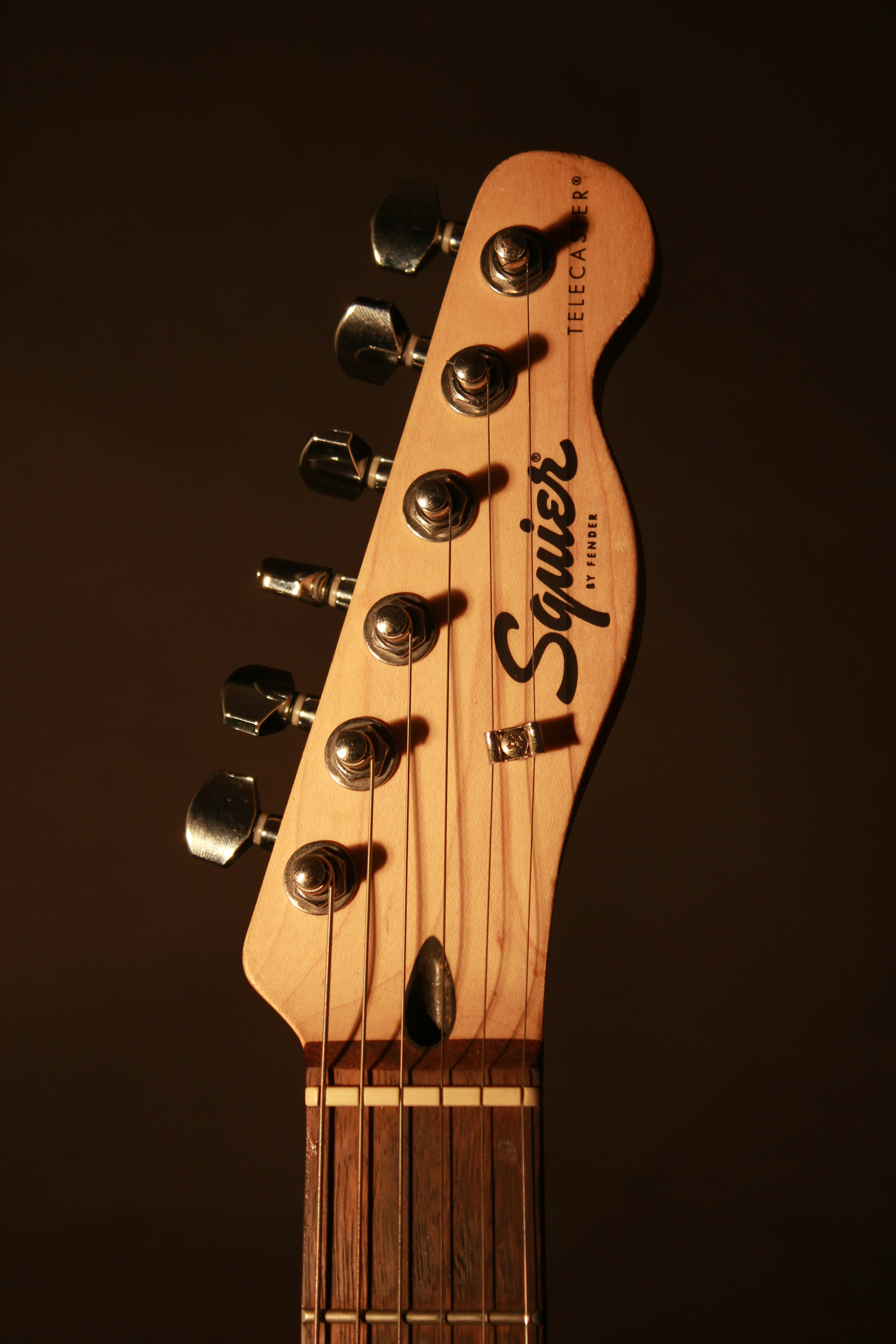 Close-up of a guitar headstock: vintage wood, tuning pegs, and strings in warm light