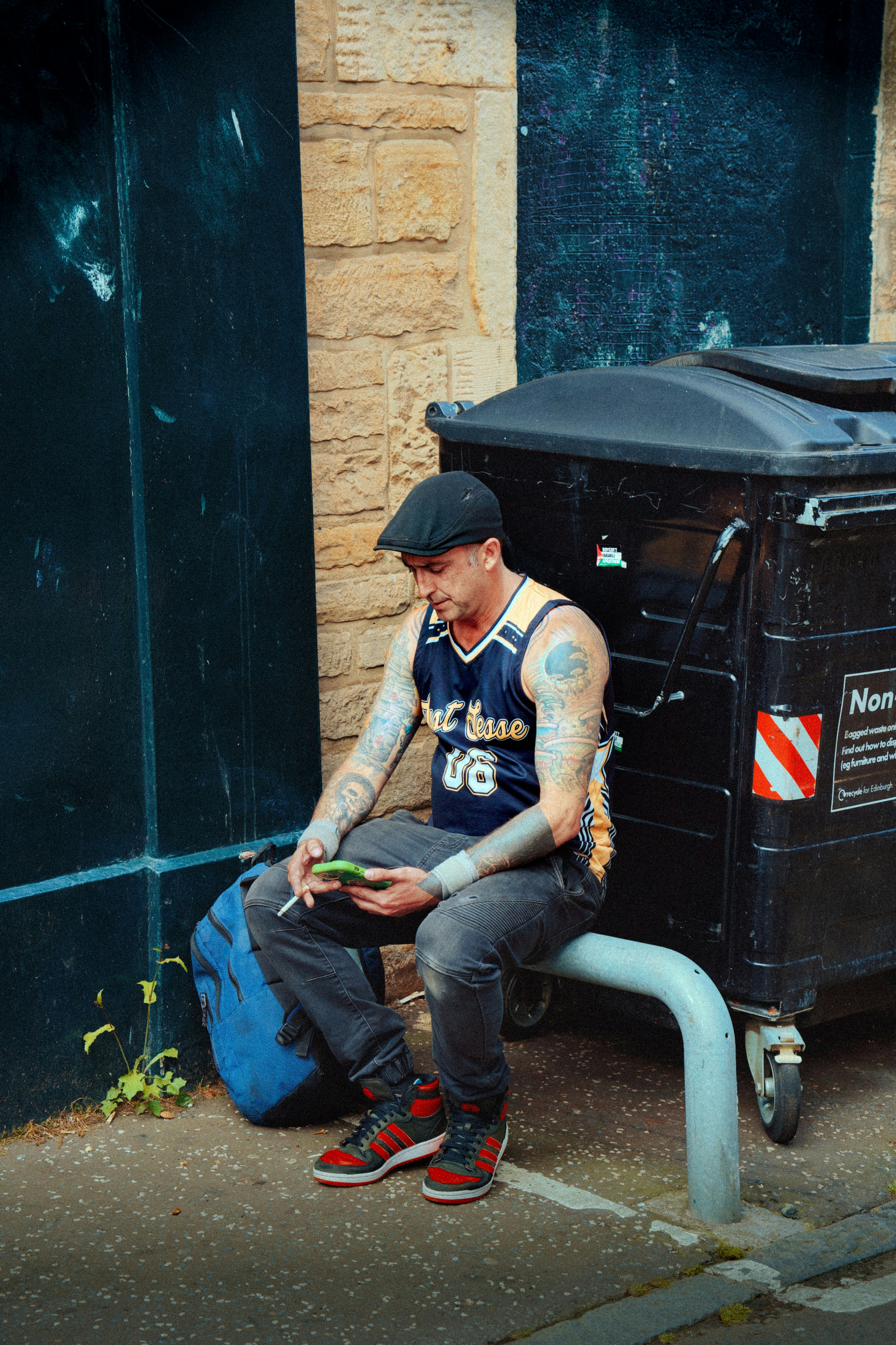 Man on the curb with phone beside a trash bin