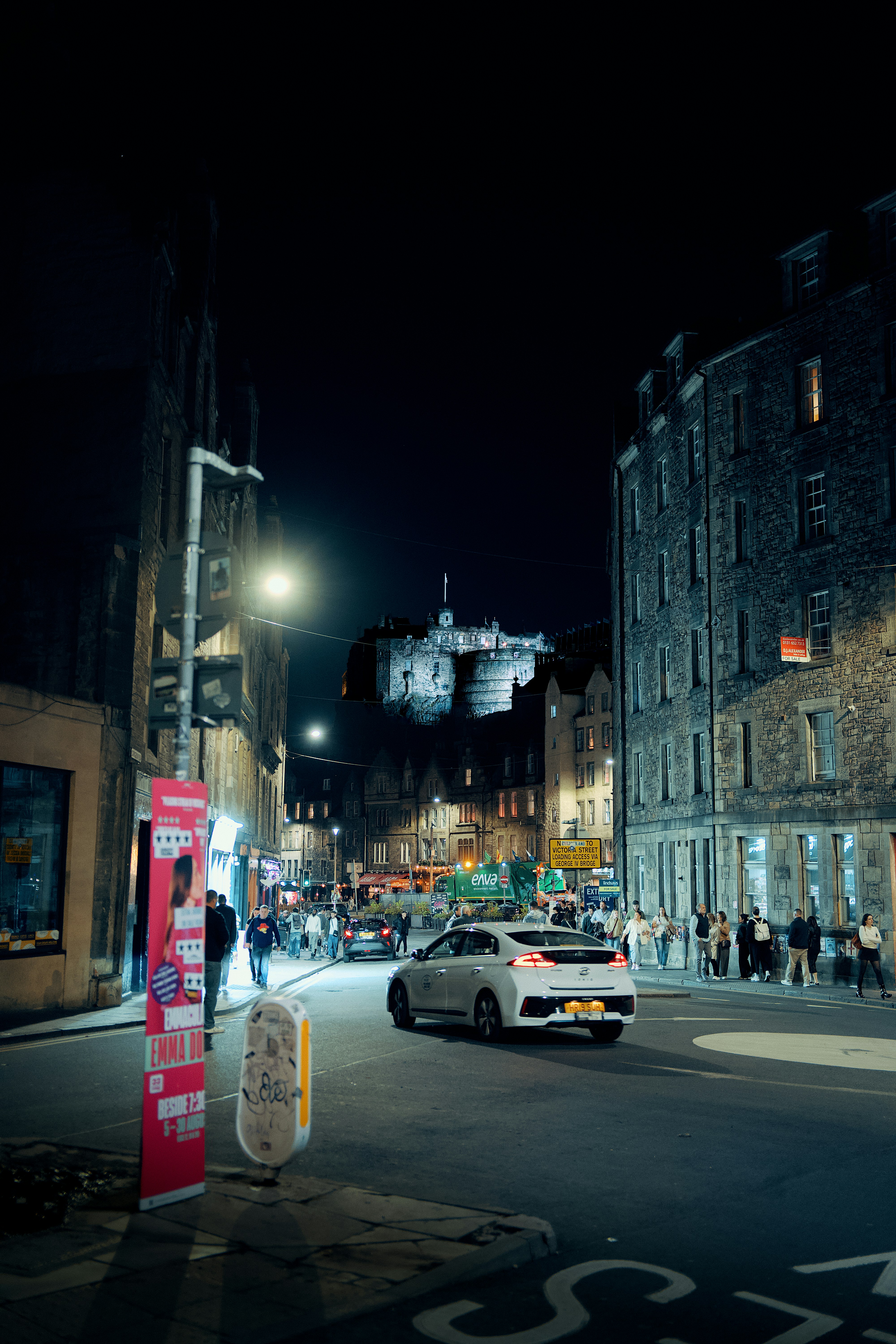 Nightfall in a Historic Street: Cars, Pedestrians, and a Castle in the Distance