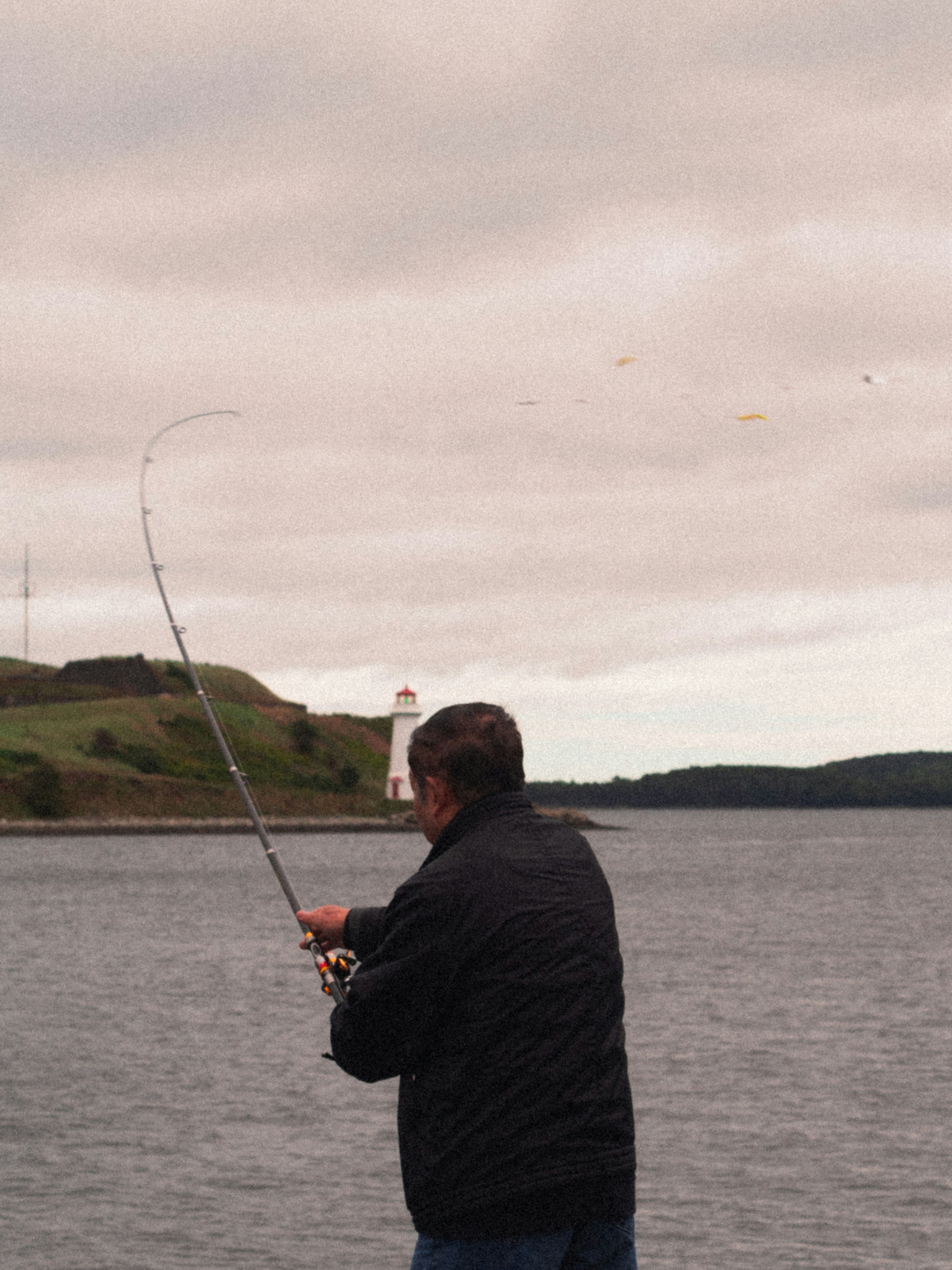 Line and Lure: A Fisherman’s Focus Against a Seaside Lighthouse