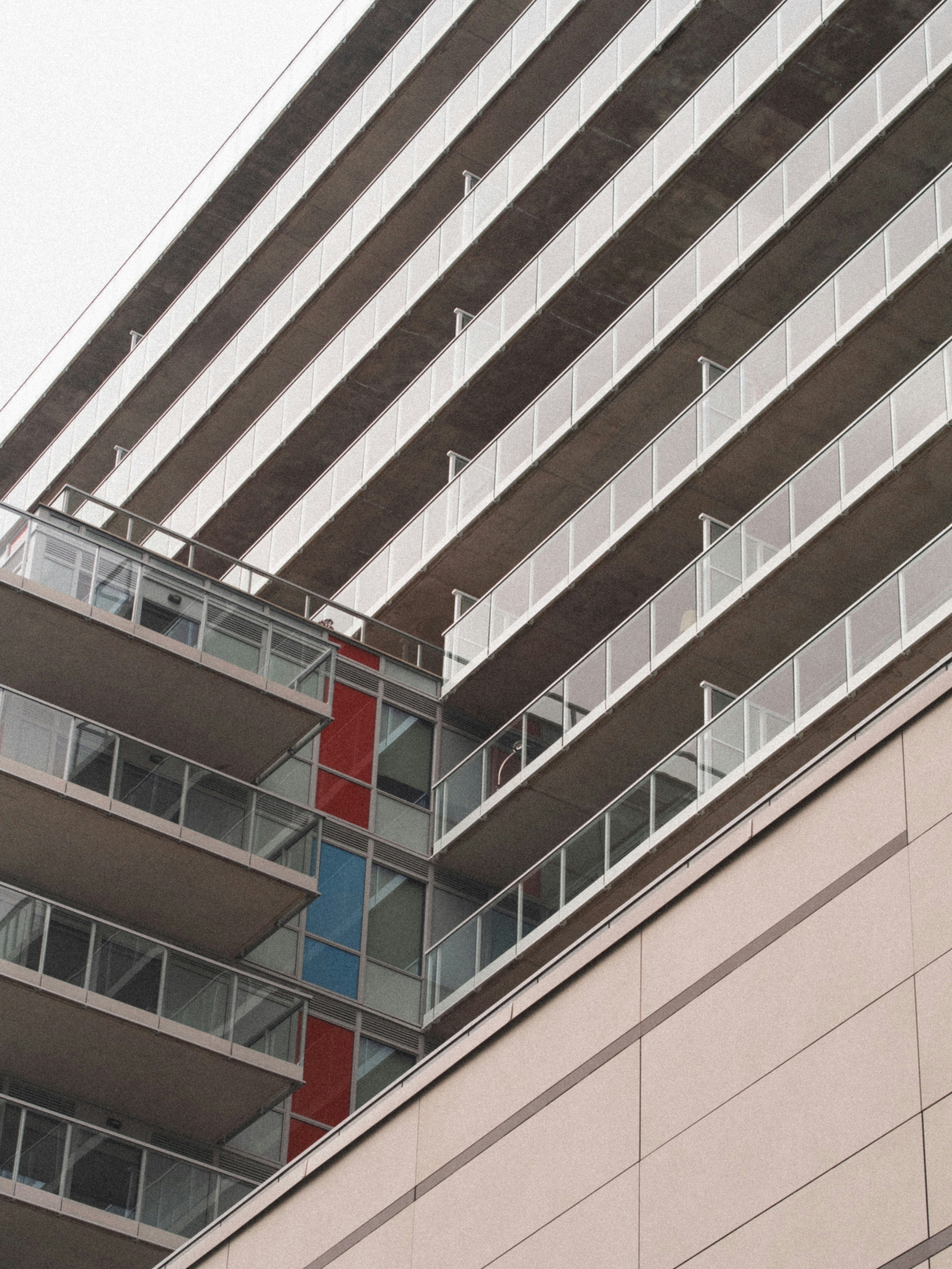 Geometric facade of a contemporary building with stacked balconies and vertical color accents in a diagonal perspective.