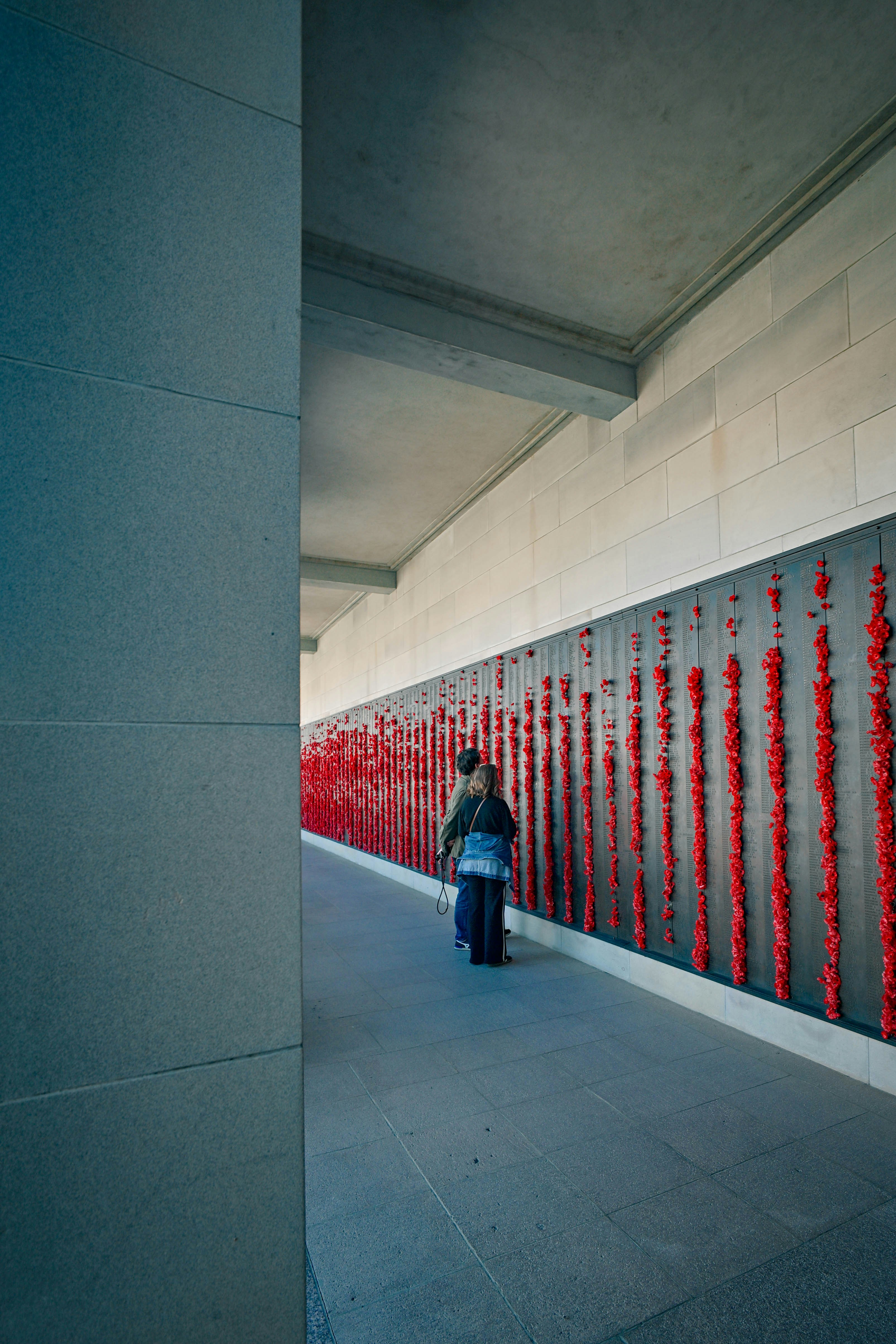 People stand before a long wall lined with vertical red strings in a modern, minimalist corridor.
