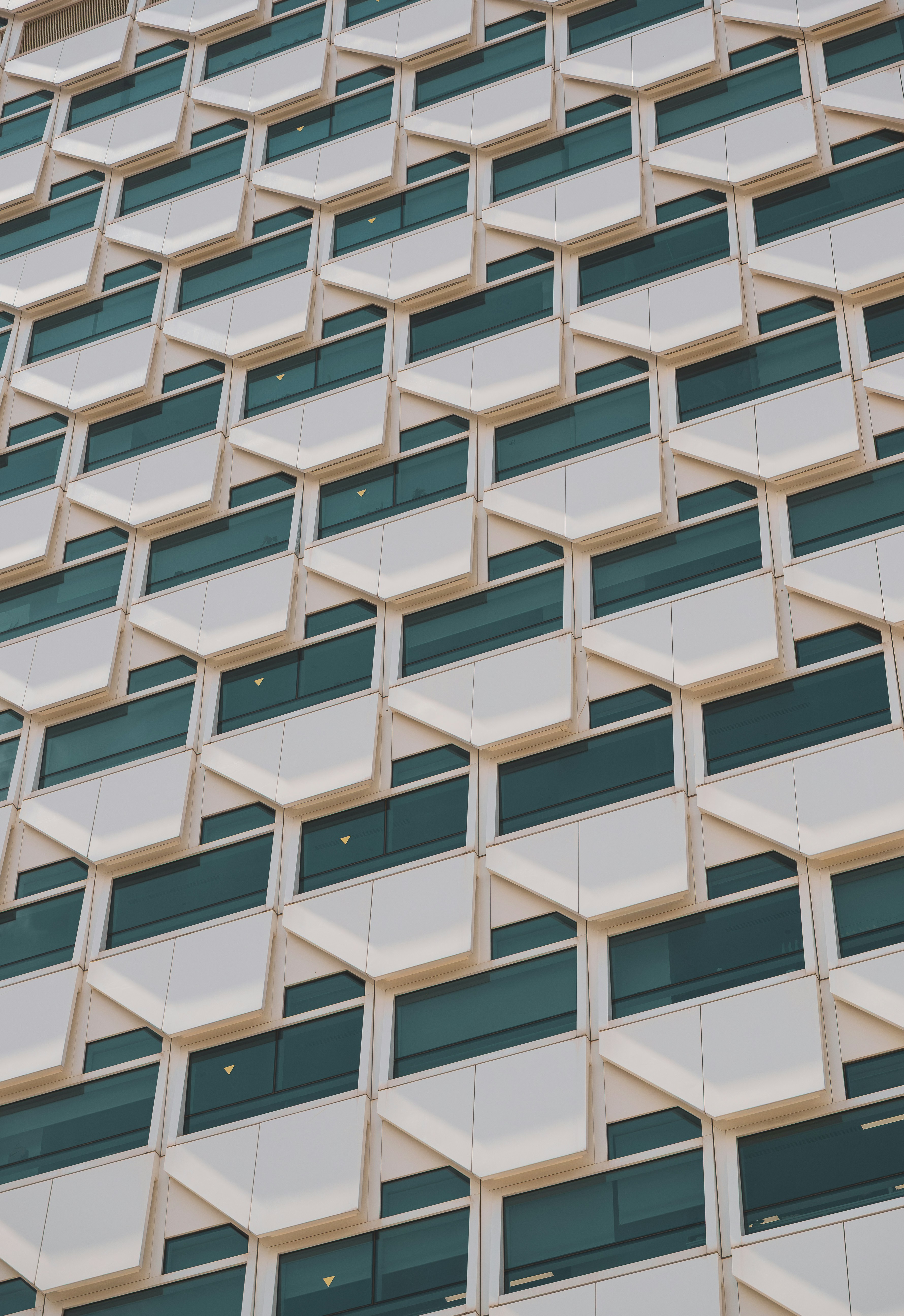 Elevated view of a modern facade with a repeating cube-like pattern of protruding windows and teal glass, highlighting architectural rhythm and texture.