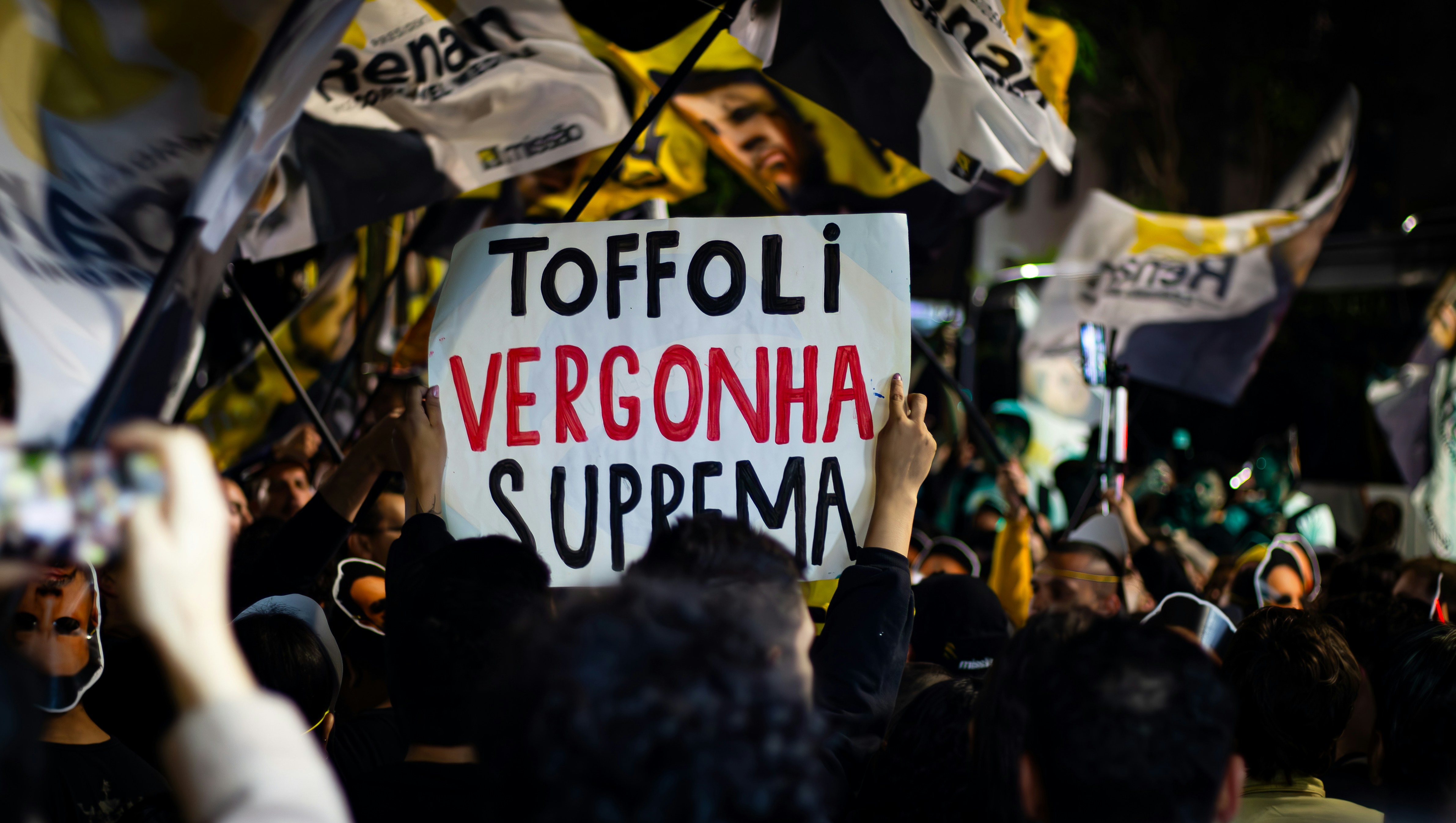 Crowd Unfolds a Protest Banner Among Nighttime Flags
