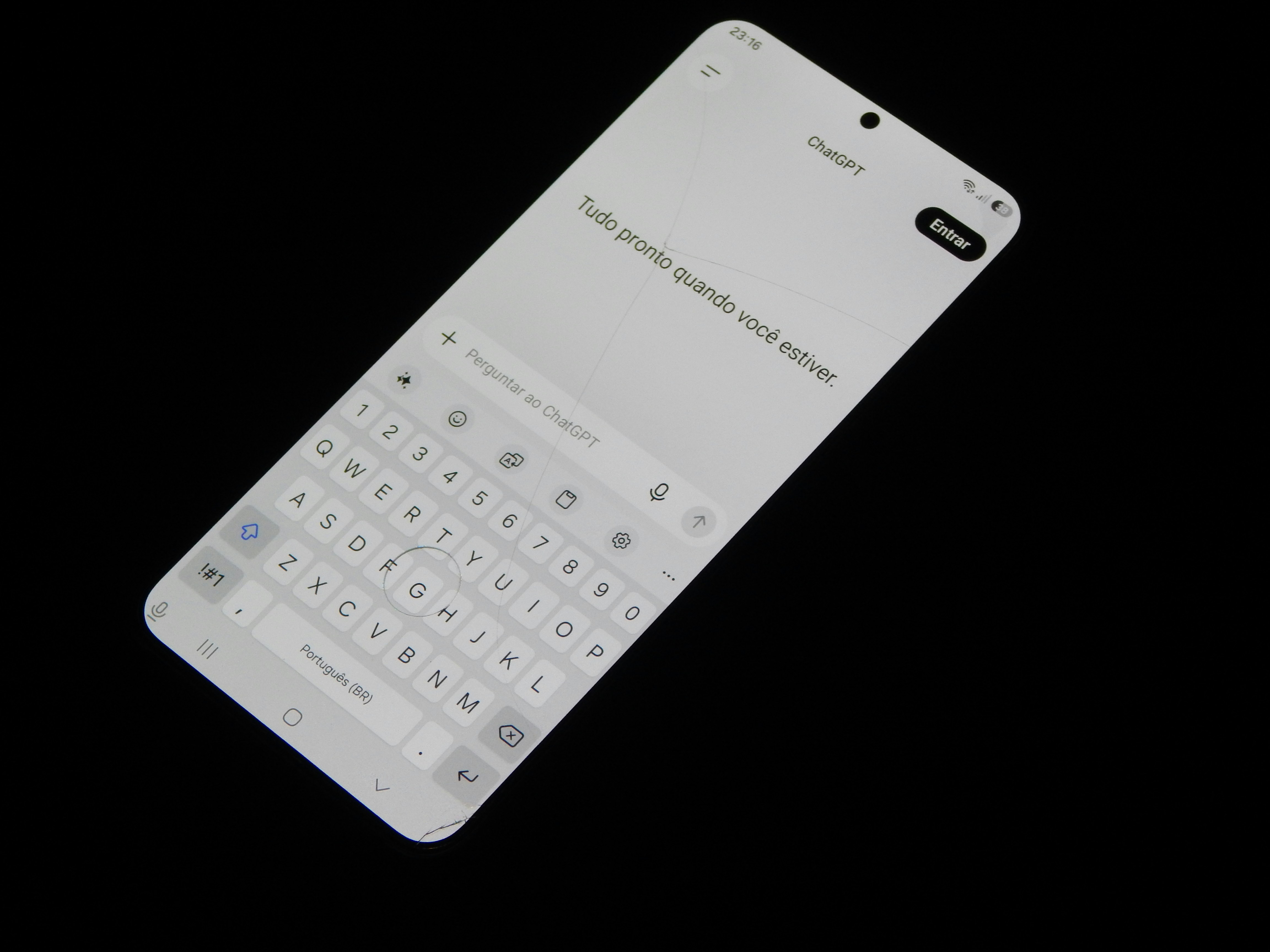 A lone smartphone rests on a dark surface, its illuminated screen showing a messaging app. The device lies at an angle, emphasizing the curved edges and soft backlight, with a clean, monochrome composition.
