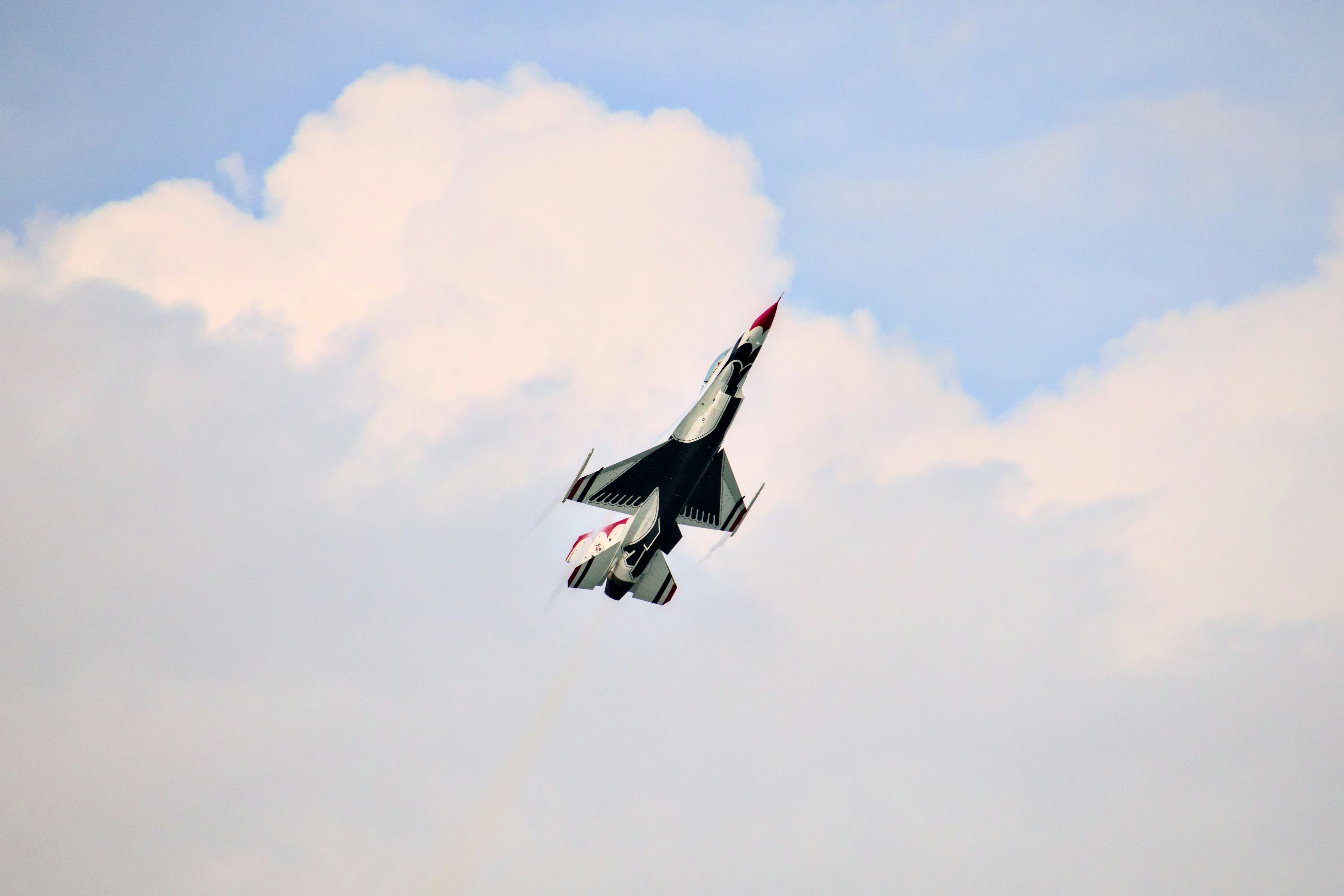A jet-like aircraft climbs through pale blue sky with wispy clouds, leaving a faint contrail behind. The image captures a dynamic ascent and the subject is isolated against the airy backdrop.