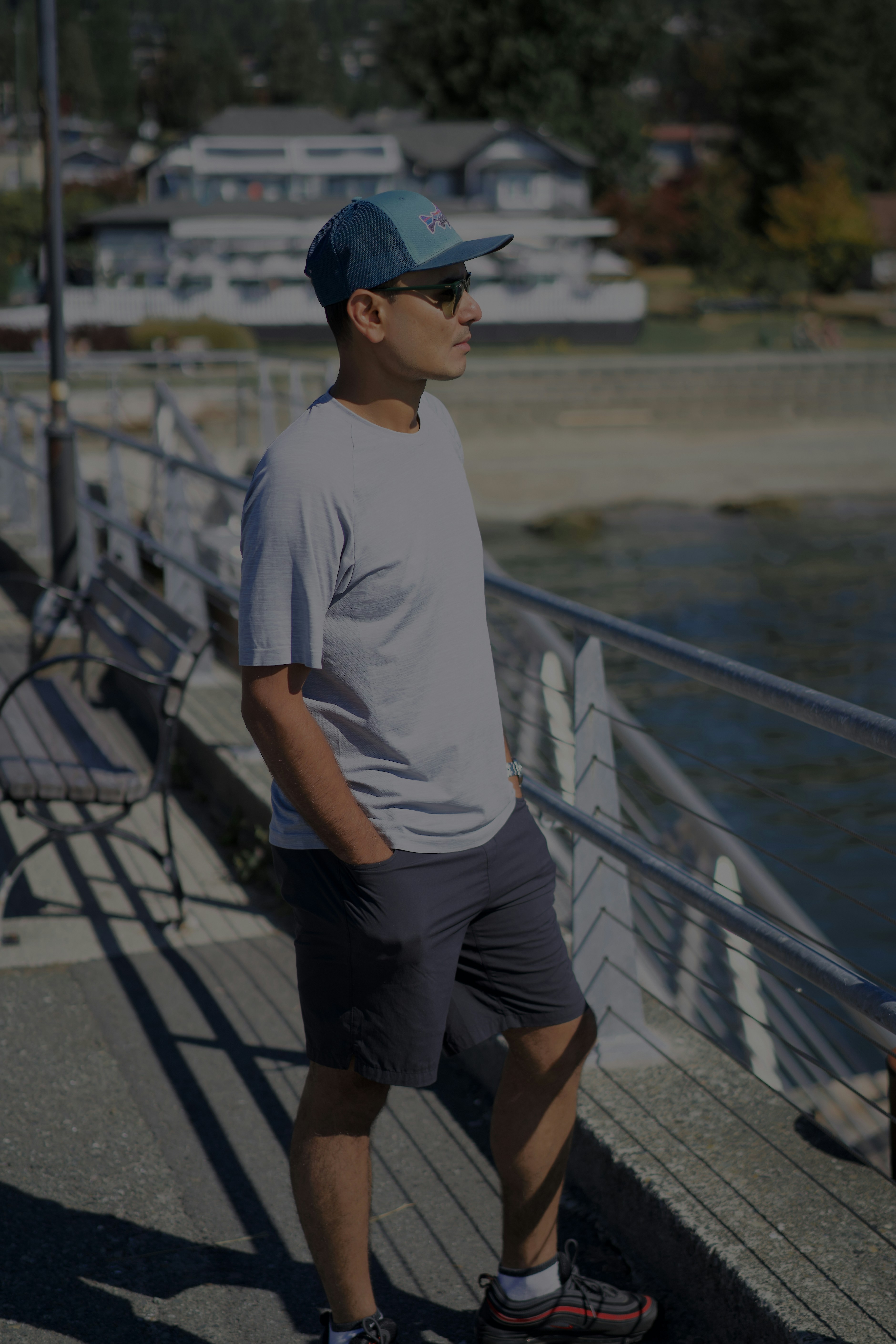 Lone figure on a waterfront overlook, shaded by cap and sunglasses