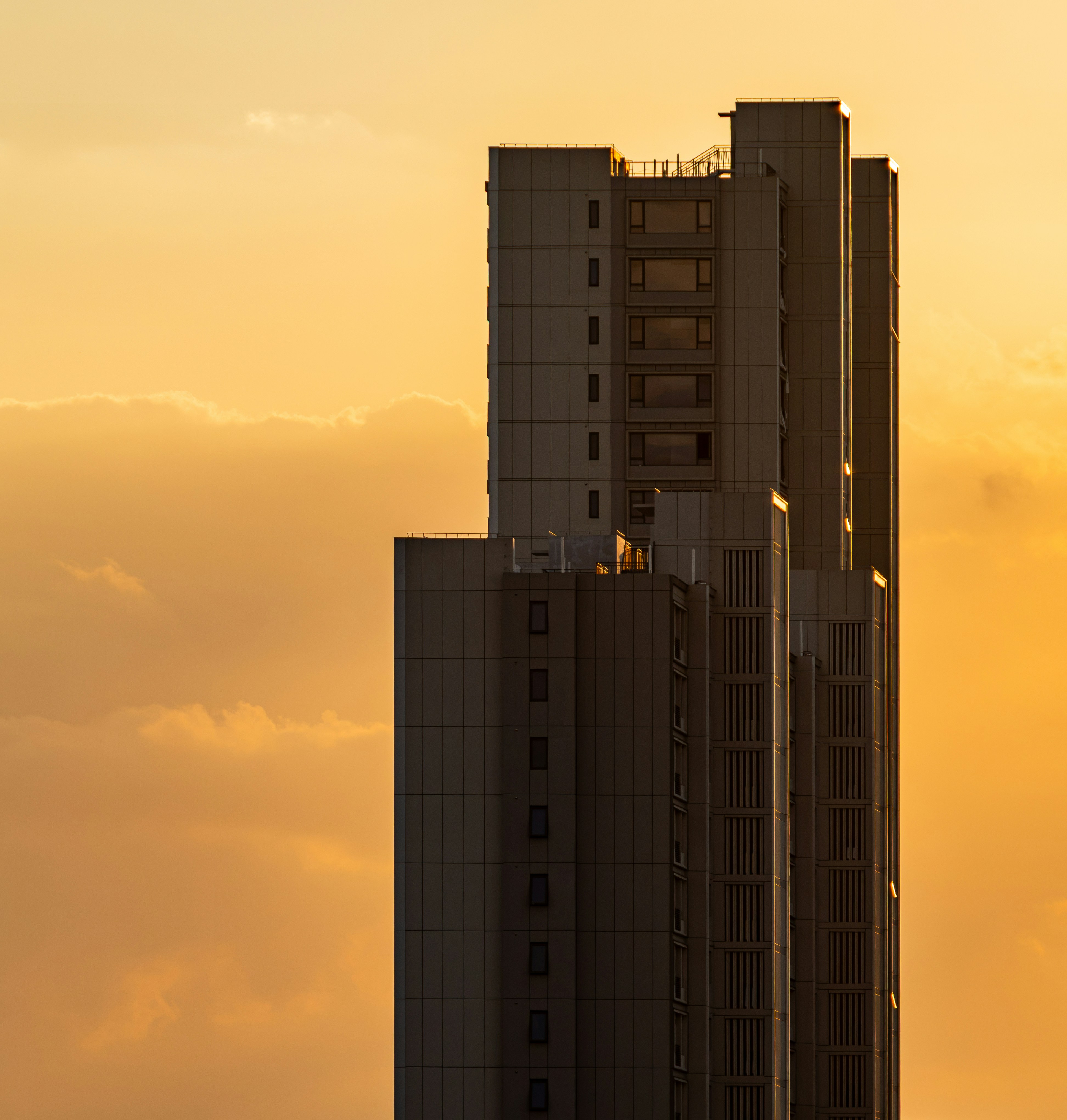 A towering skyscraper silhouette against a warm sunset sky, emphasizing the building's vertical geometry and glow along the edges.