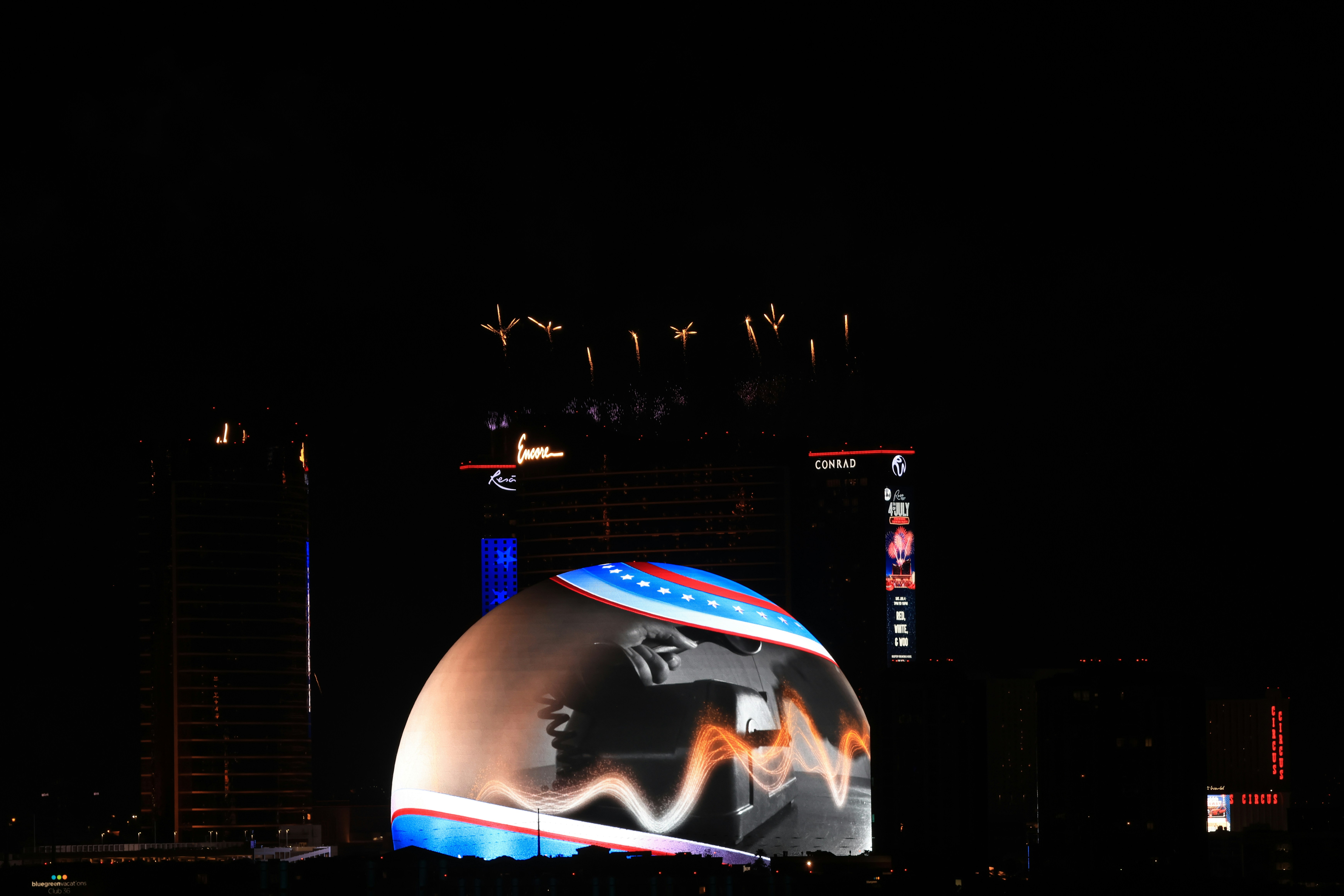 Giant illuminated amphitheater dome beneath a skyline of midnight high-rrises